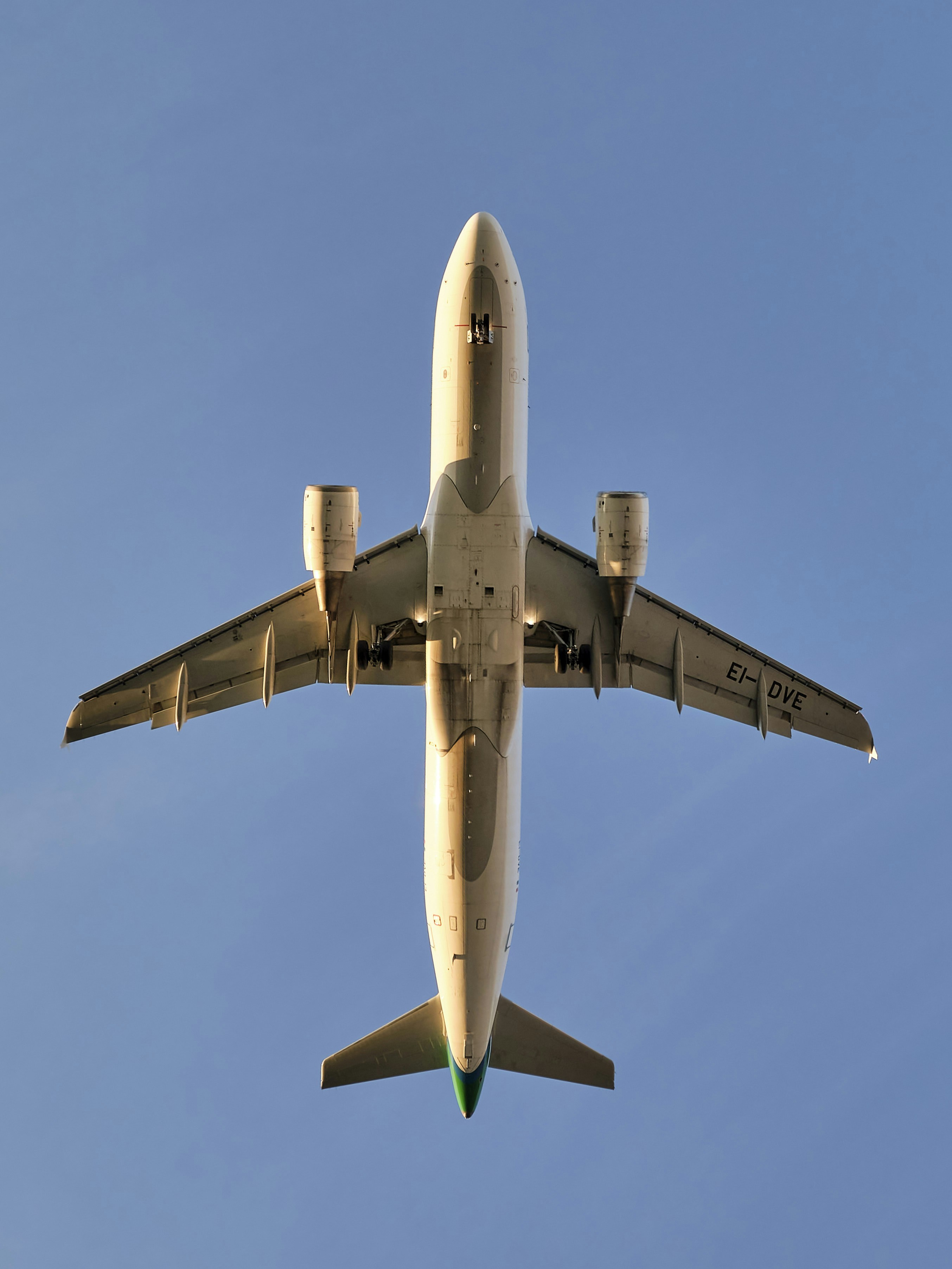 Commercial aircraft captured from below against a clear blue sky, showcasing its underbelly and wing structure.
