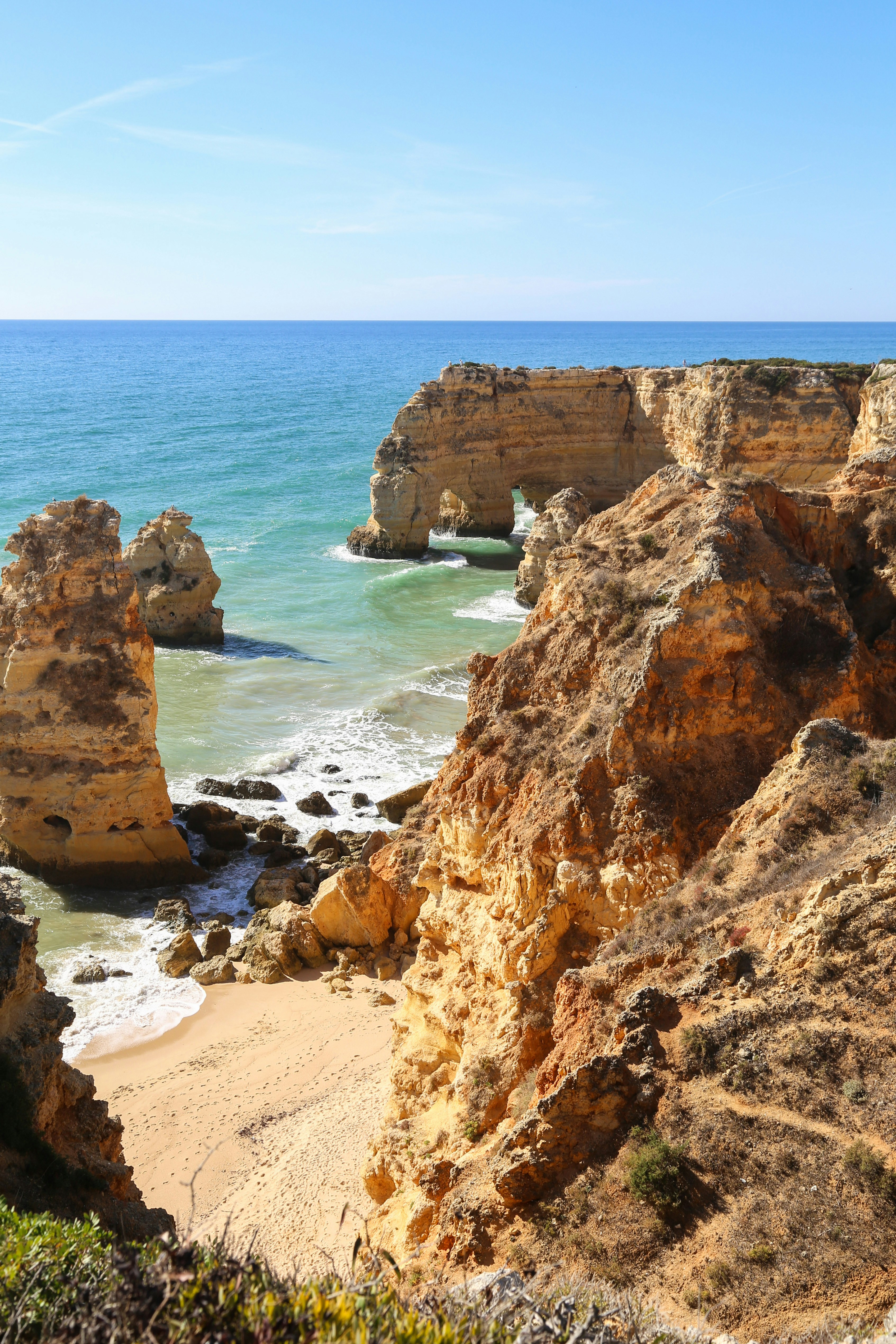 Golden cliffs rise majestically above the turquoise sea, framing a secluded sandy beach below. Natural rock formations create a stunning coastal landscape.