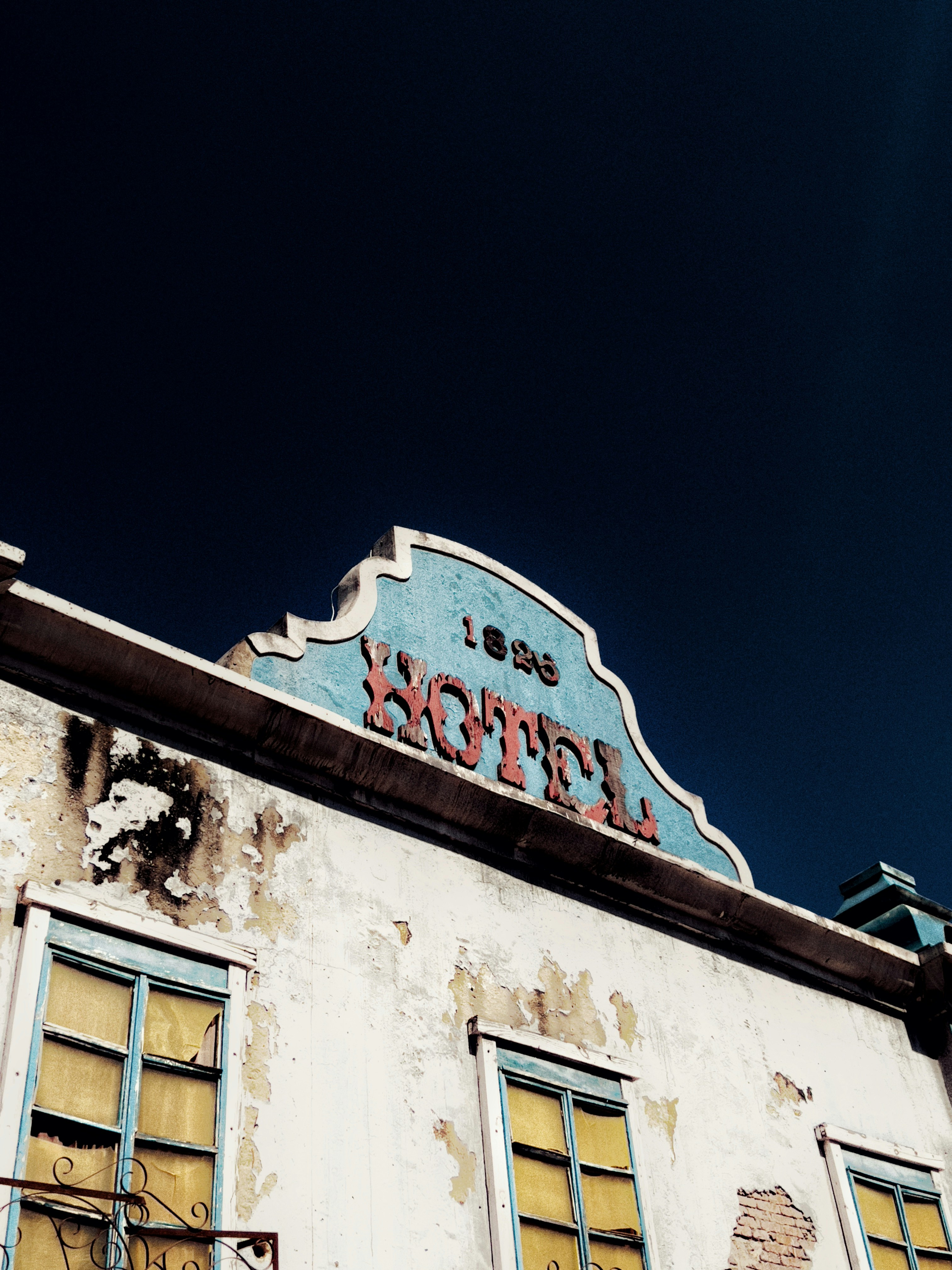 Weathered hotel facade from 1880 showcasing peeling paint and vintage signage against a deep blue sky.