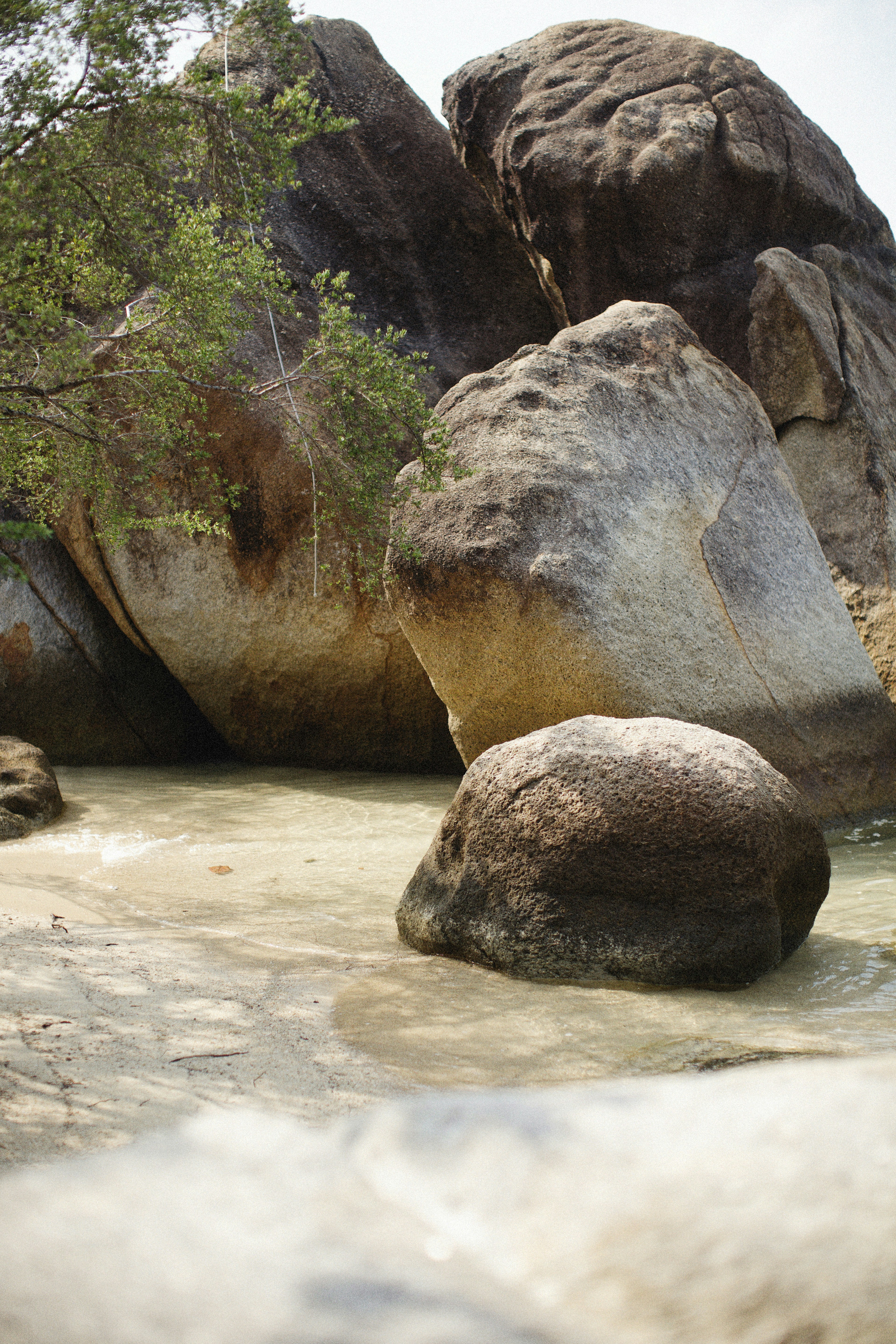 Large granite boulders partially submerged in shallow water, surrounded by lush greenery and a serene atmosphere.