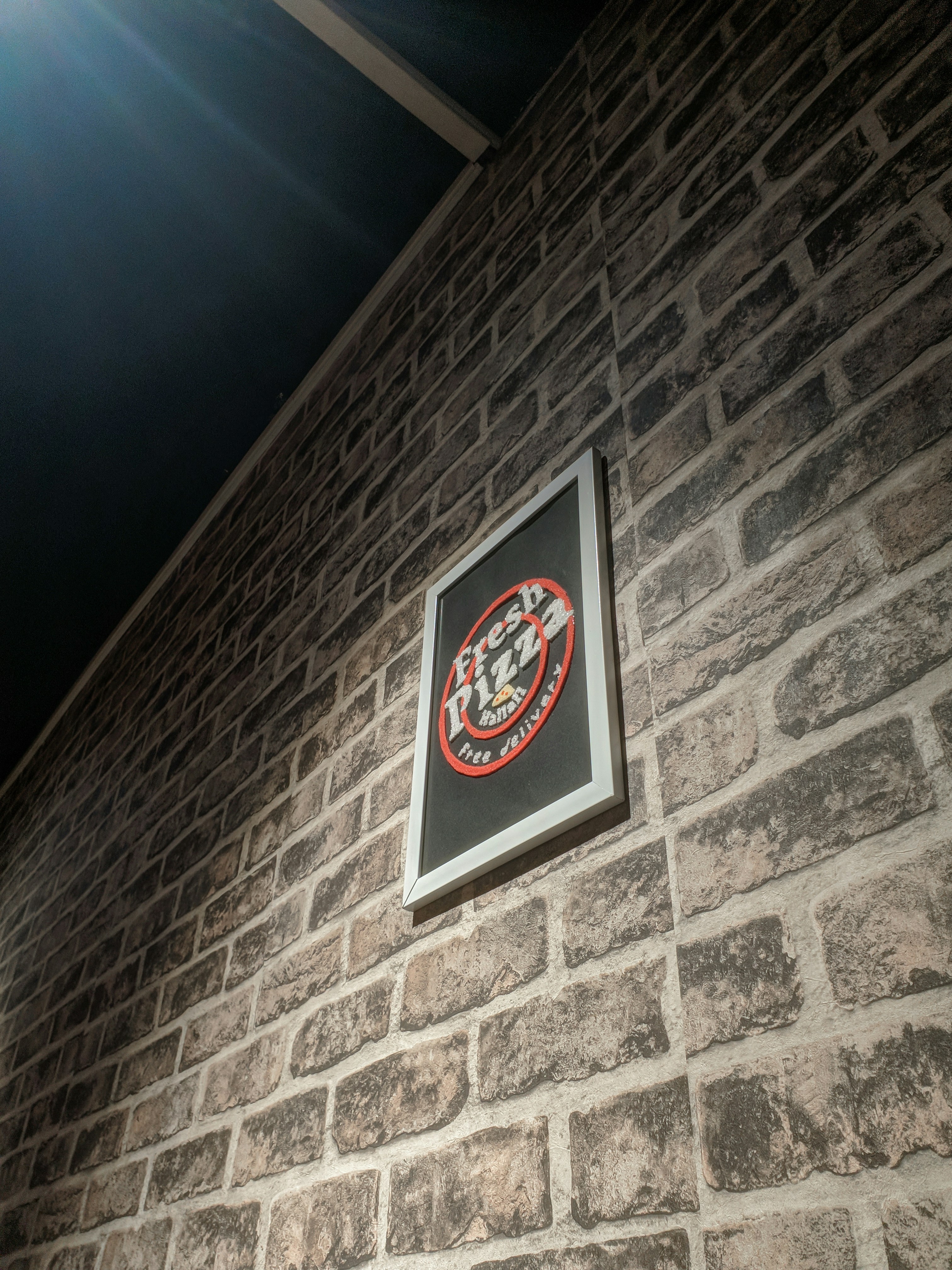 Logo of a pizza restaurant displayed on a textured brick wall, illuminated by overhead lighting.