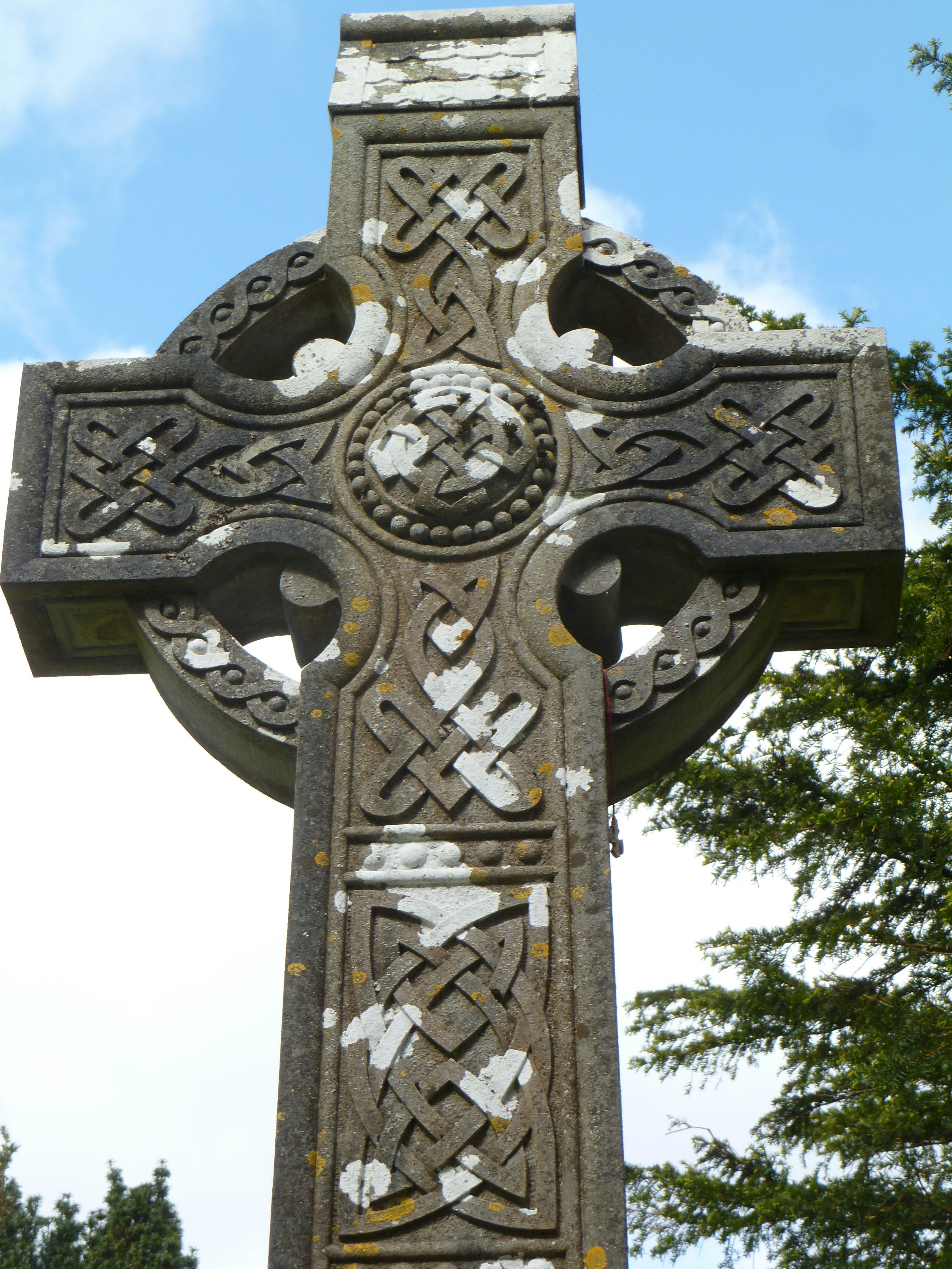 Intricate Celtic cross adorned with weathered carvings and lichen, set against a bright blue sky.