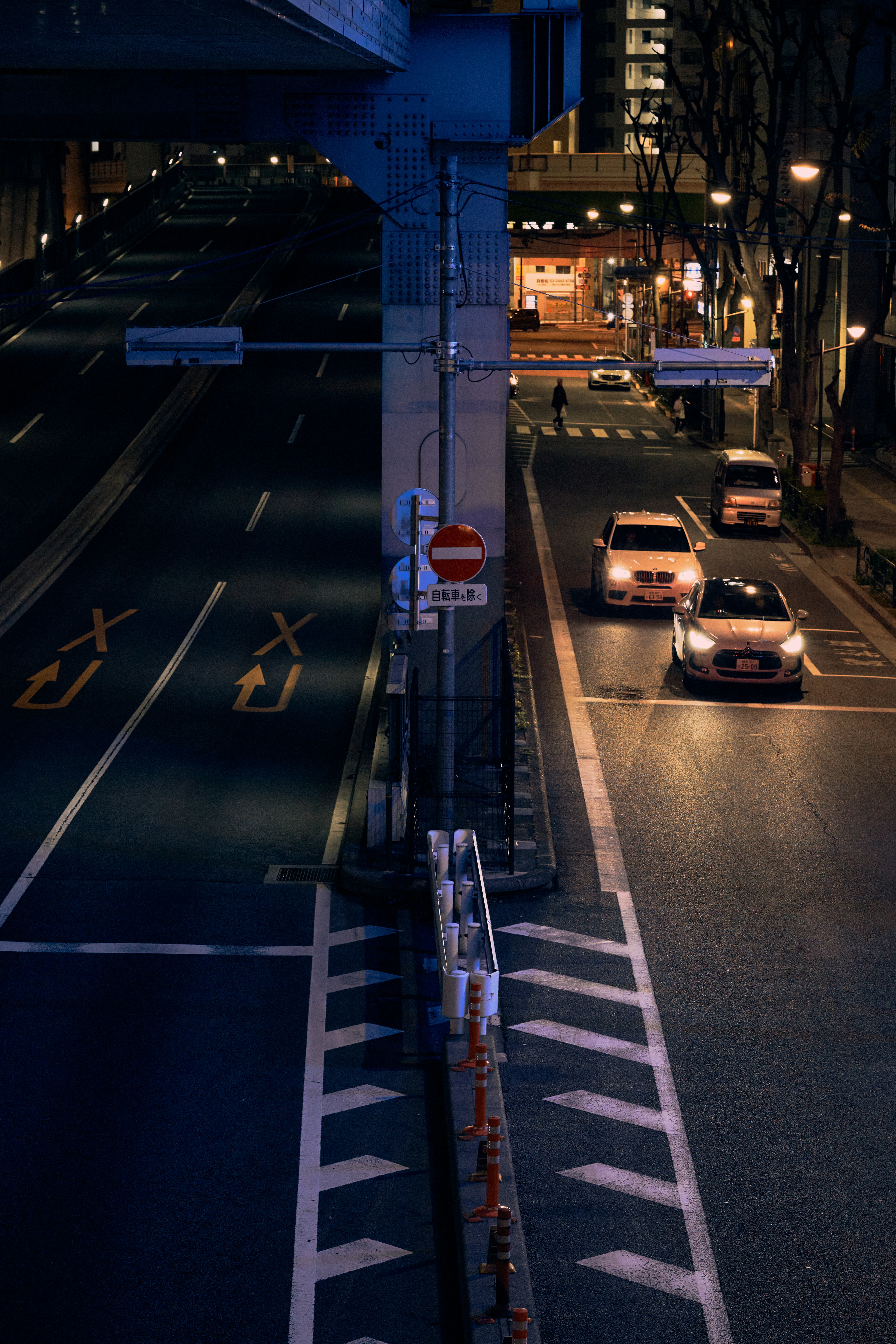 Nighttime cityscape featuring illuminated streets and vehicles navigating under an overpass. The scene captures the essence of urban life after dark.