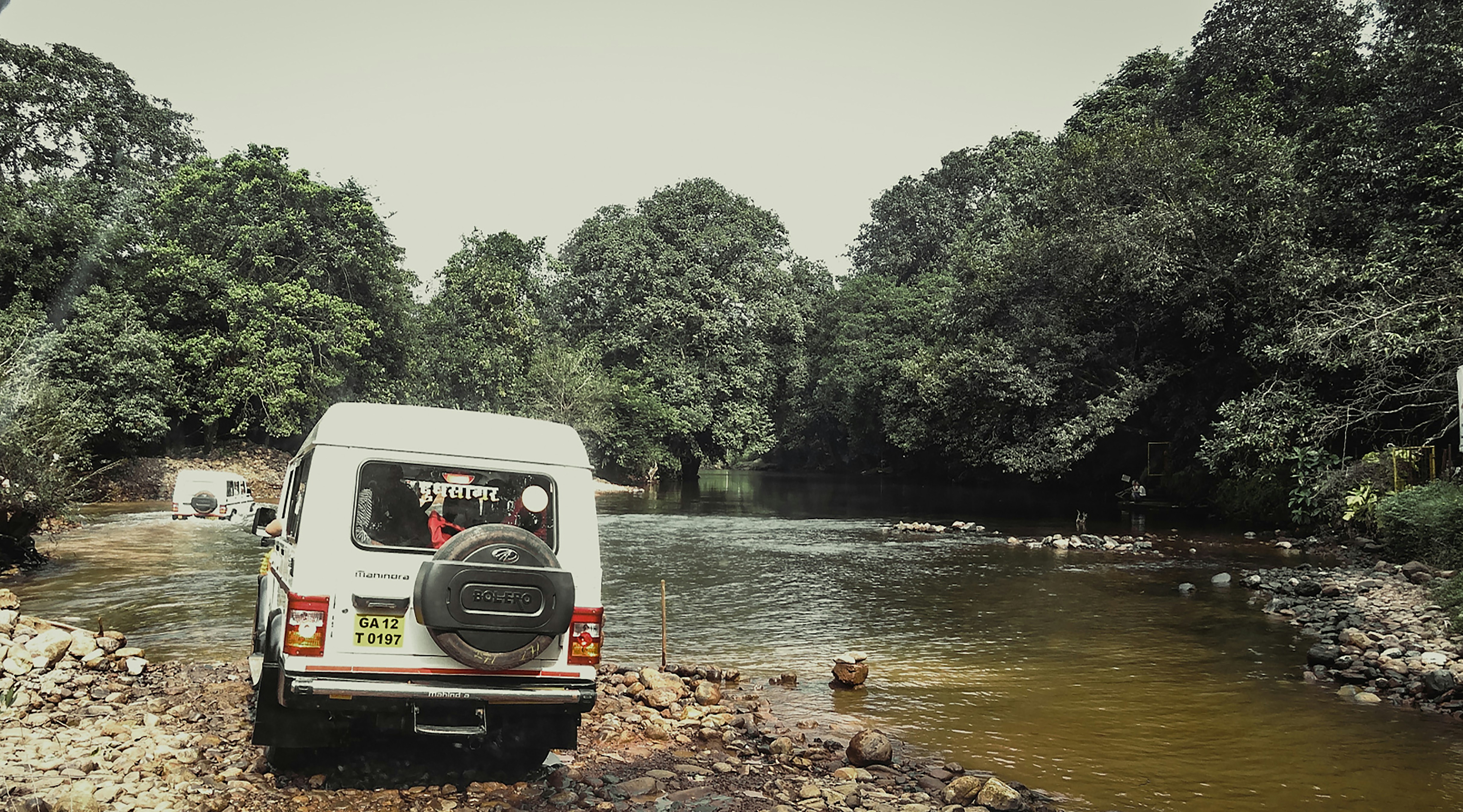 Off-road vehicle parked beside a tranquil river, surrounded by lush greenery. The scene captures a moment of exploration in nature.