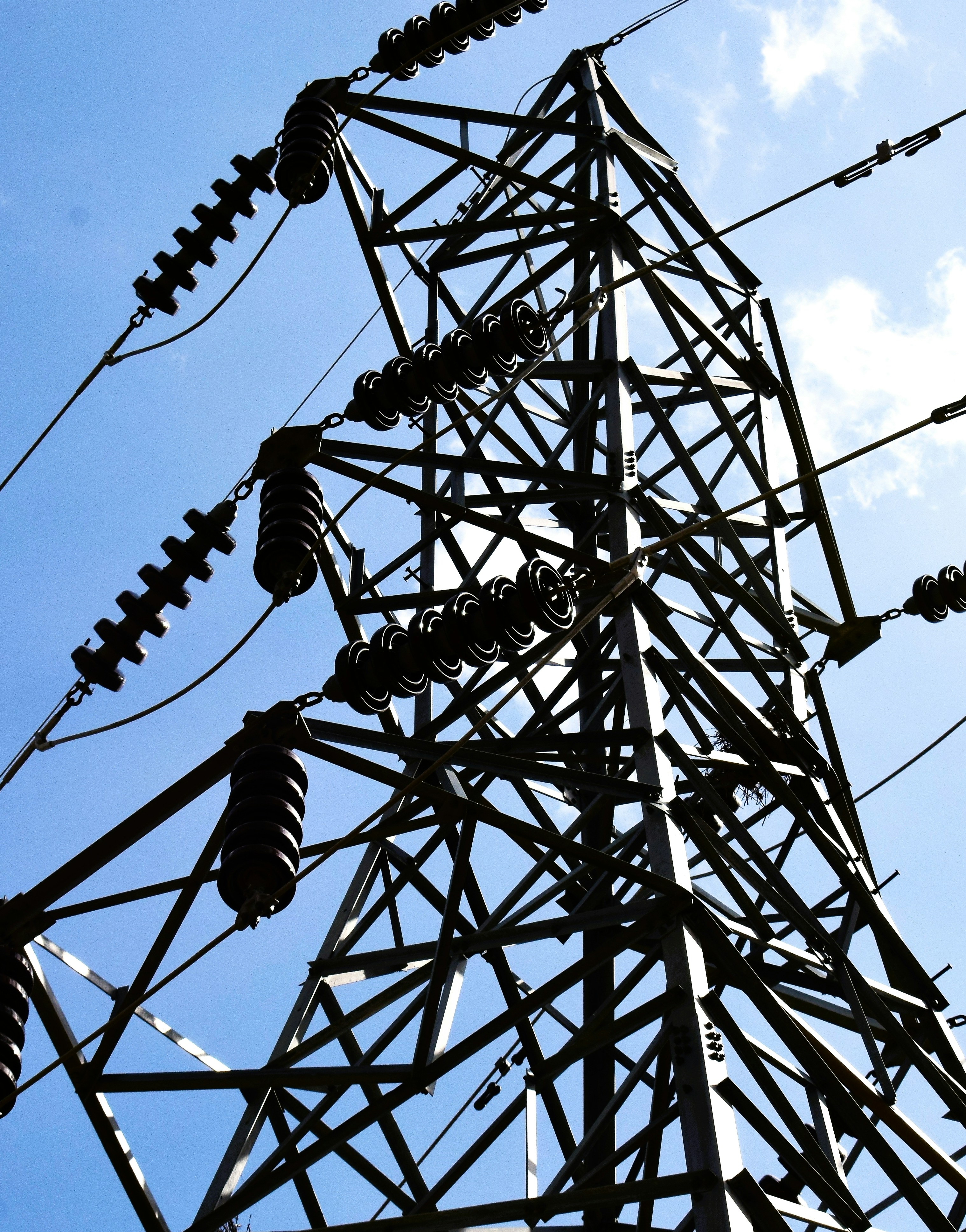 High-voltage power tower reaching towards the sky, showcasing intricate metalwork and electrical components against a bright blue backdrop.
