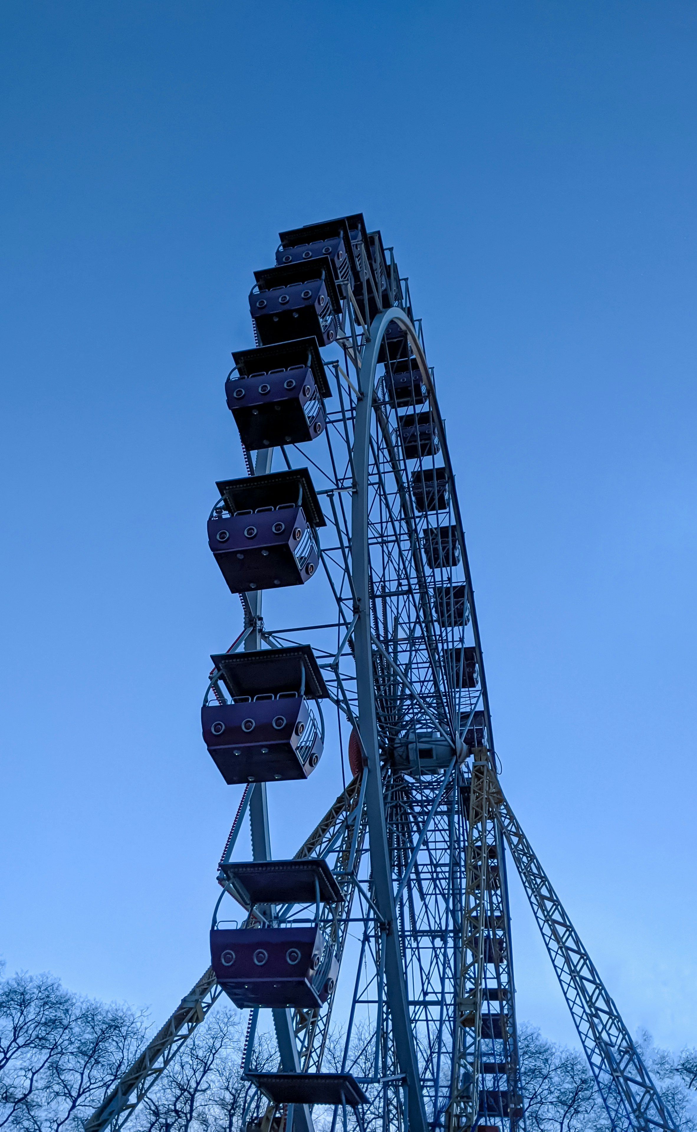 Ferris wheel towers against a pristine blue sky, with cabins marching along the rim. The scene emphasizes the wheel's geometric spokes and vertical scale.