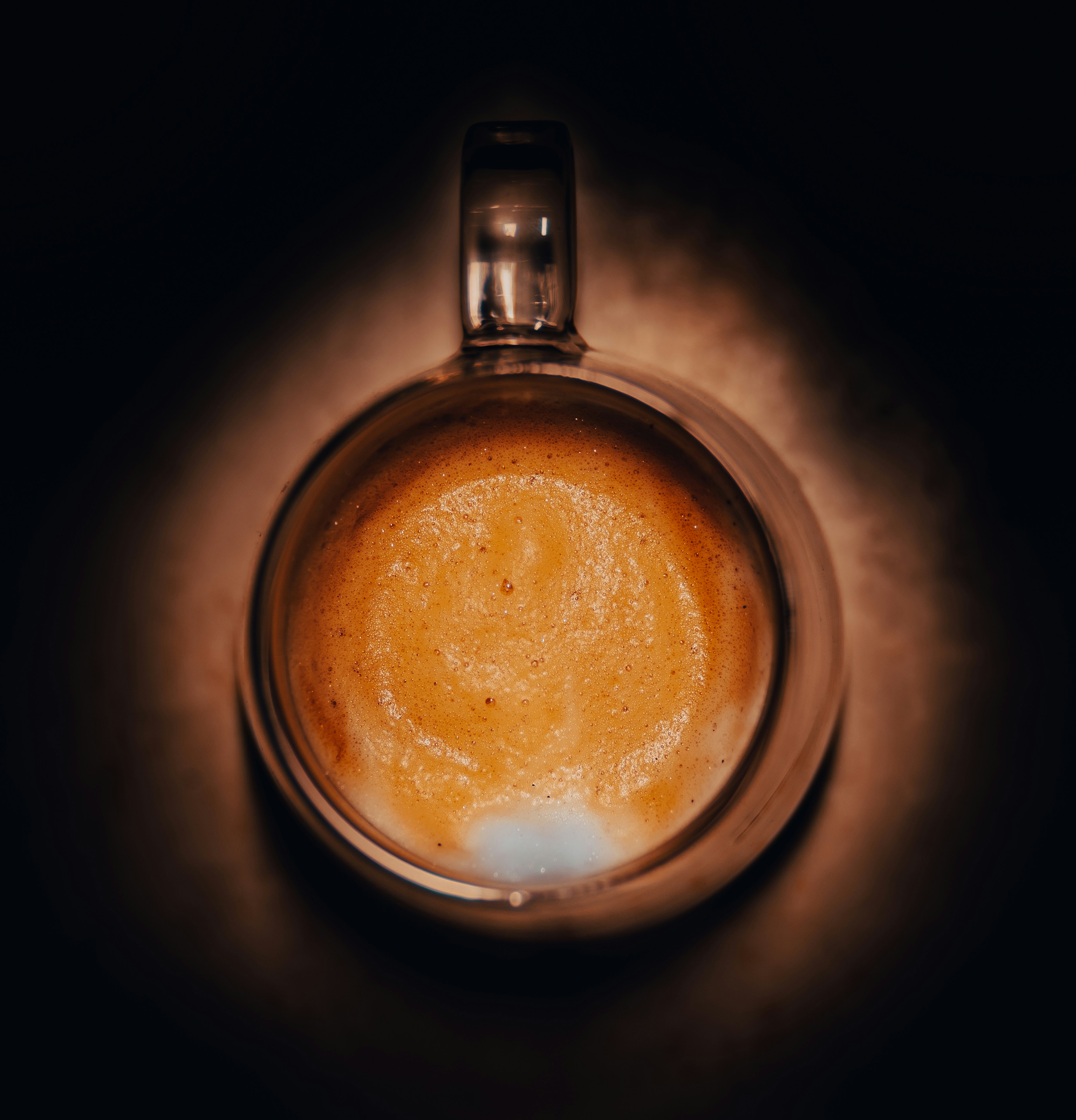 Close-up view of a coffee cup revealing intricate patterns in the frothy surface against a dark background.