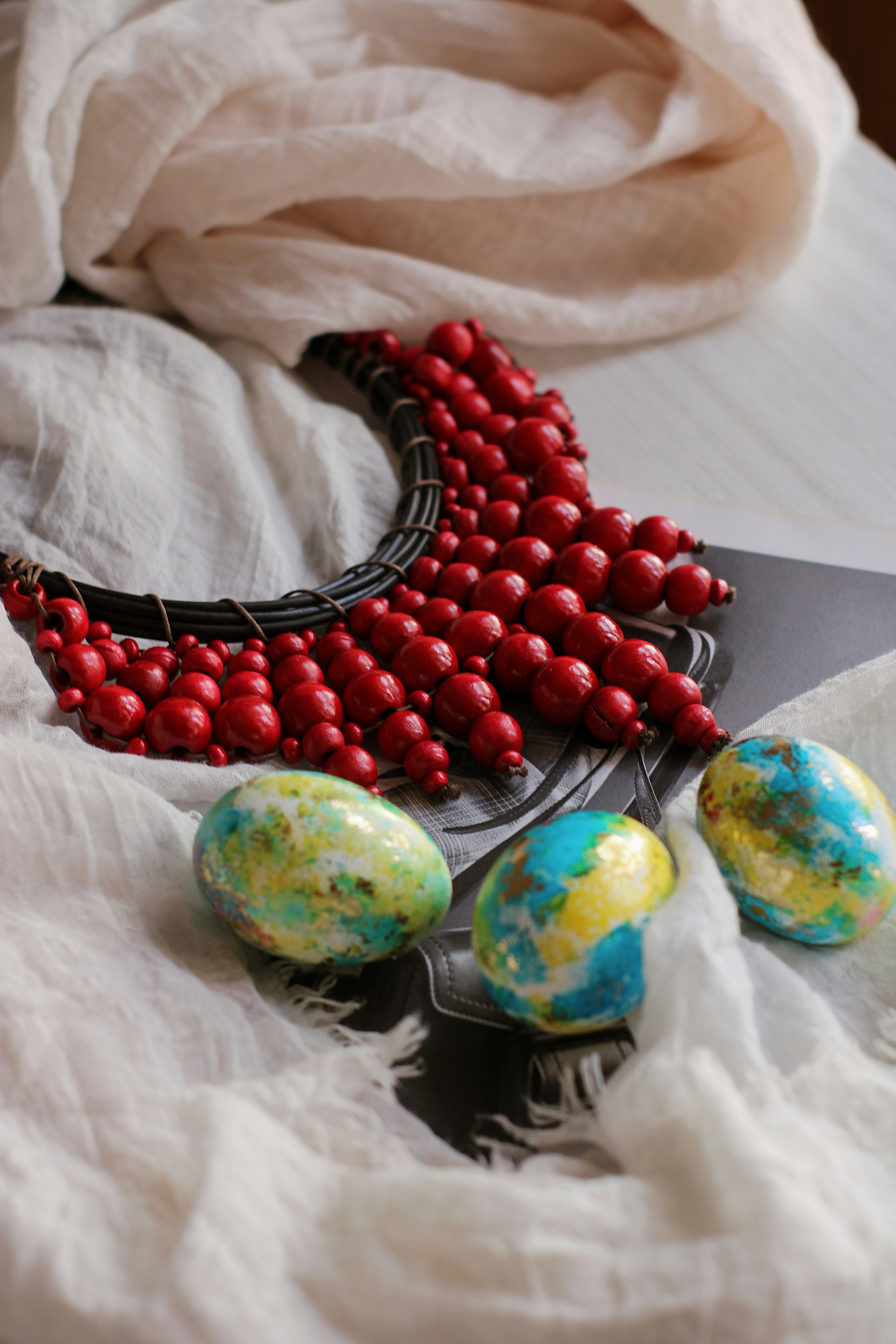 Crimson Bead Necklace Amid Silk and Globe-Pattern Eggs
