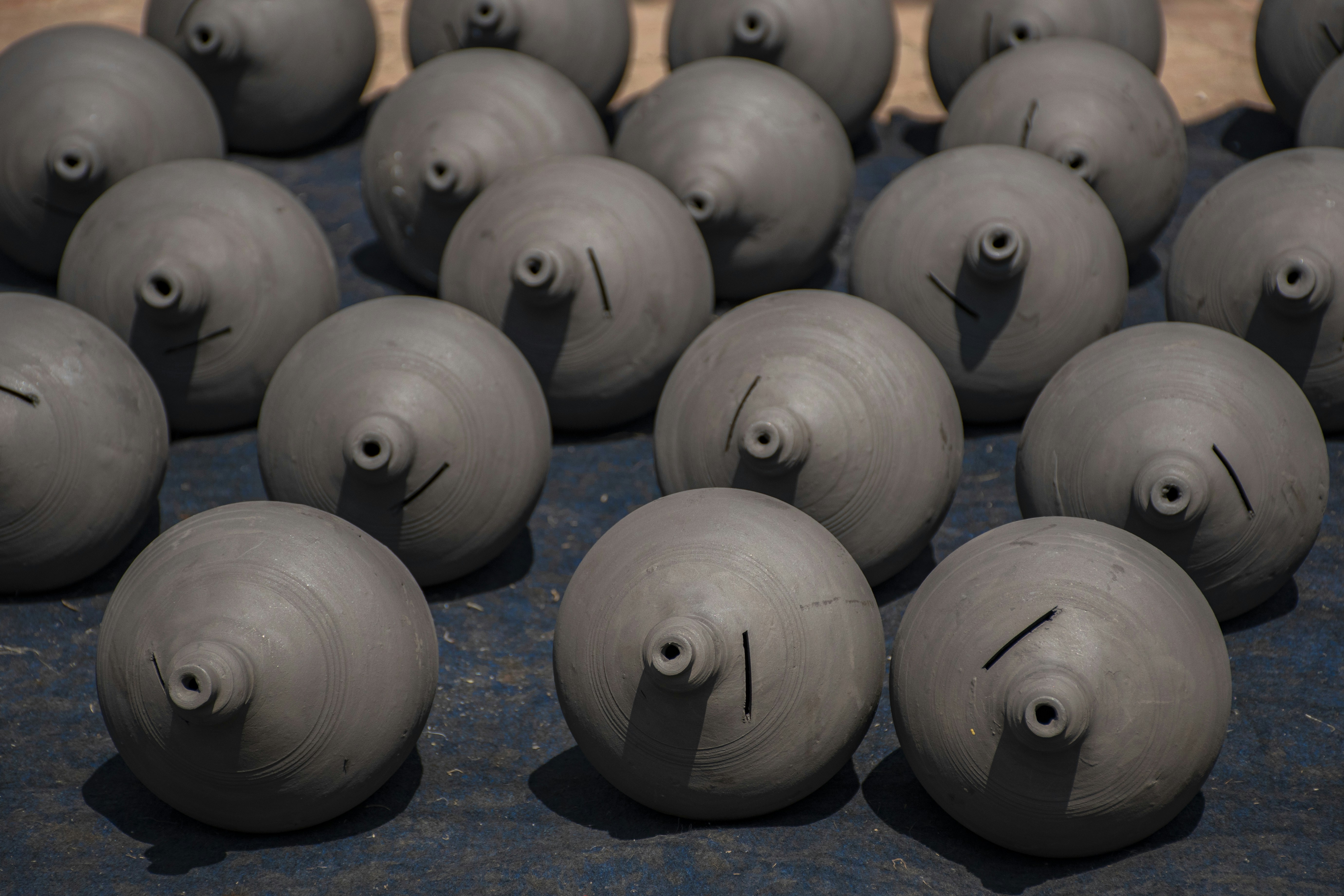 A collection of unglazed clay pots arranged in a pattern on a blue tarp, showcasing the craftsmanship of pottery making.