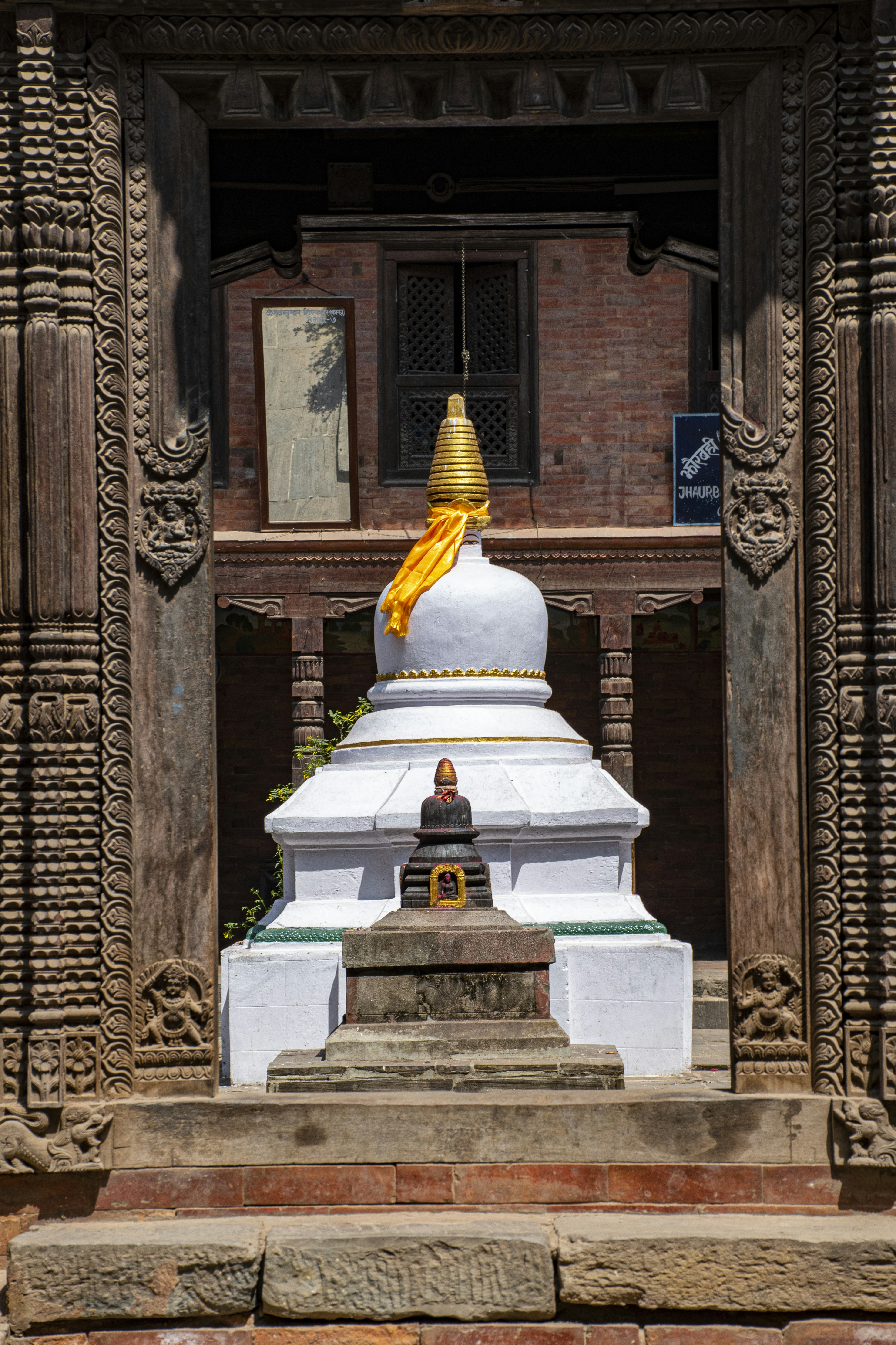 Centered Stupa Under a Carved Gateway: A Quiet Nepalese Shrine Framed by Ancient Wood