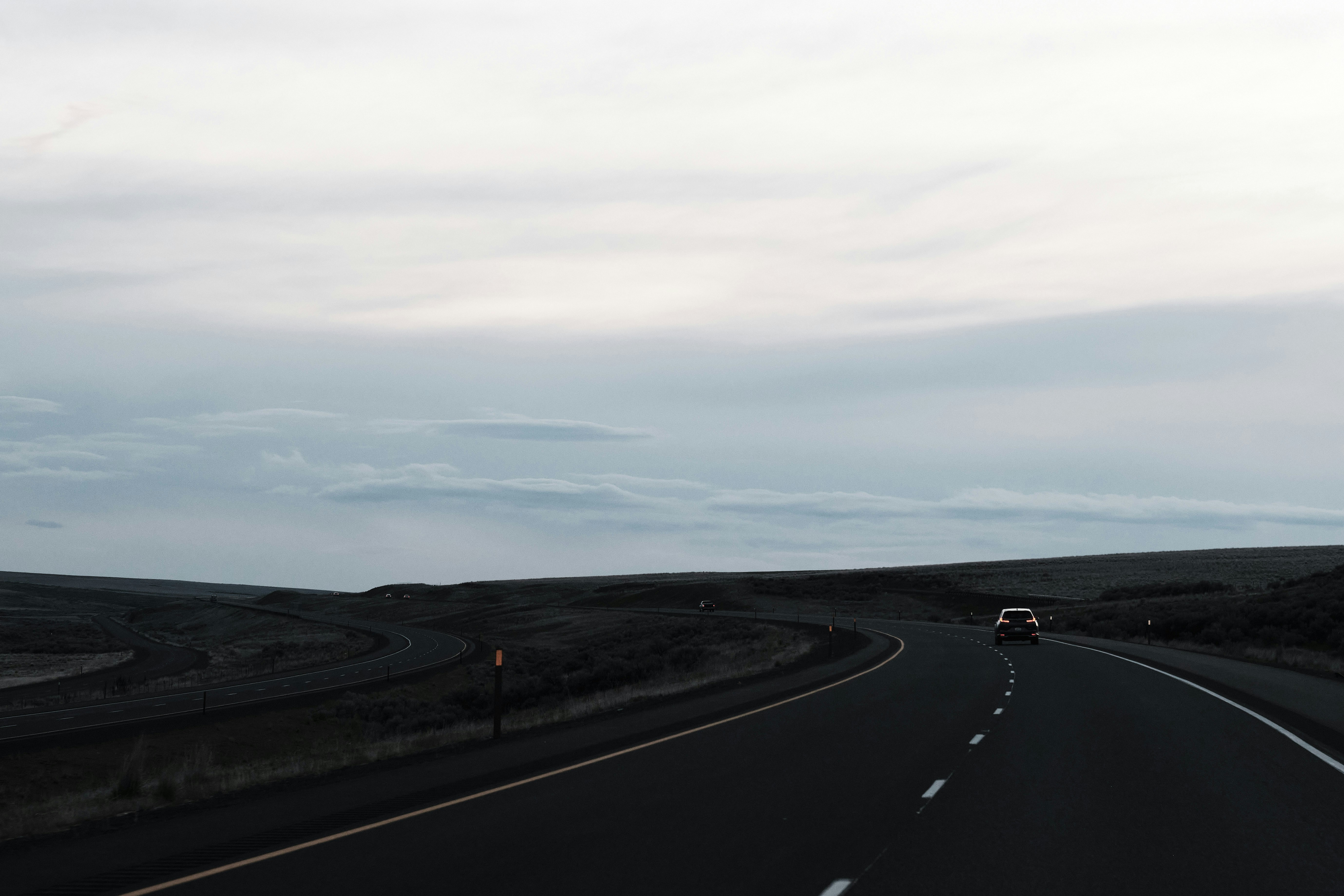 Winding highway stretches into a vast landscape under a soft, cloudy sky, hinting at the tranquility of an open road.