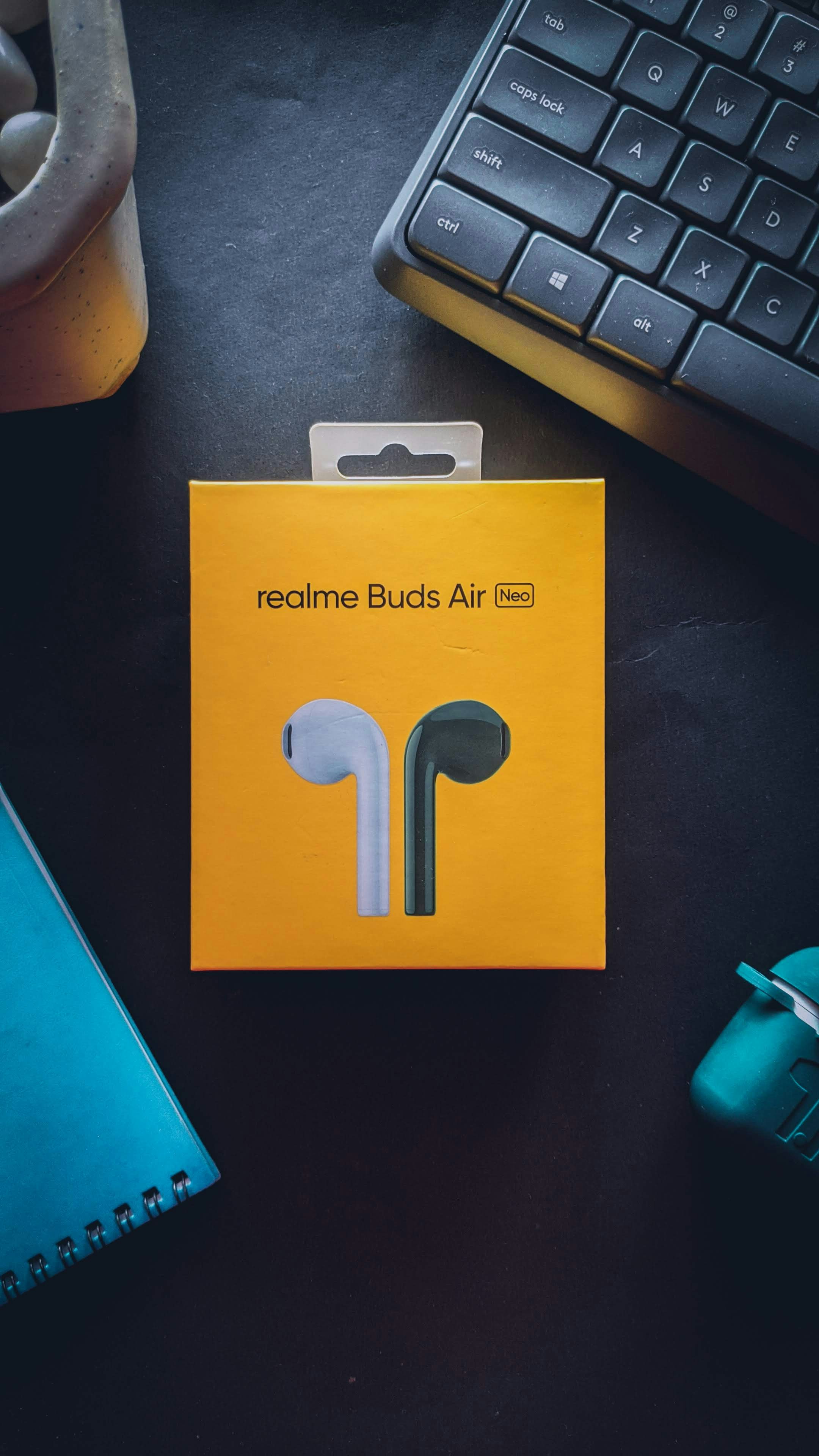 Orange Realme Buds Box on a Dark Desk with Keyboard and Accessories