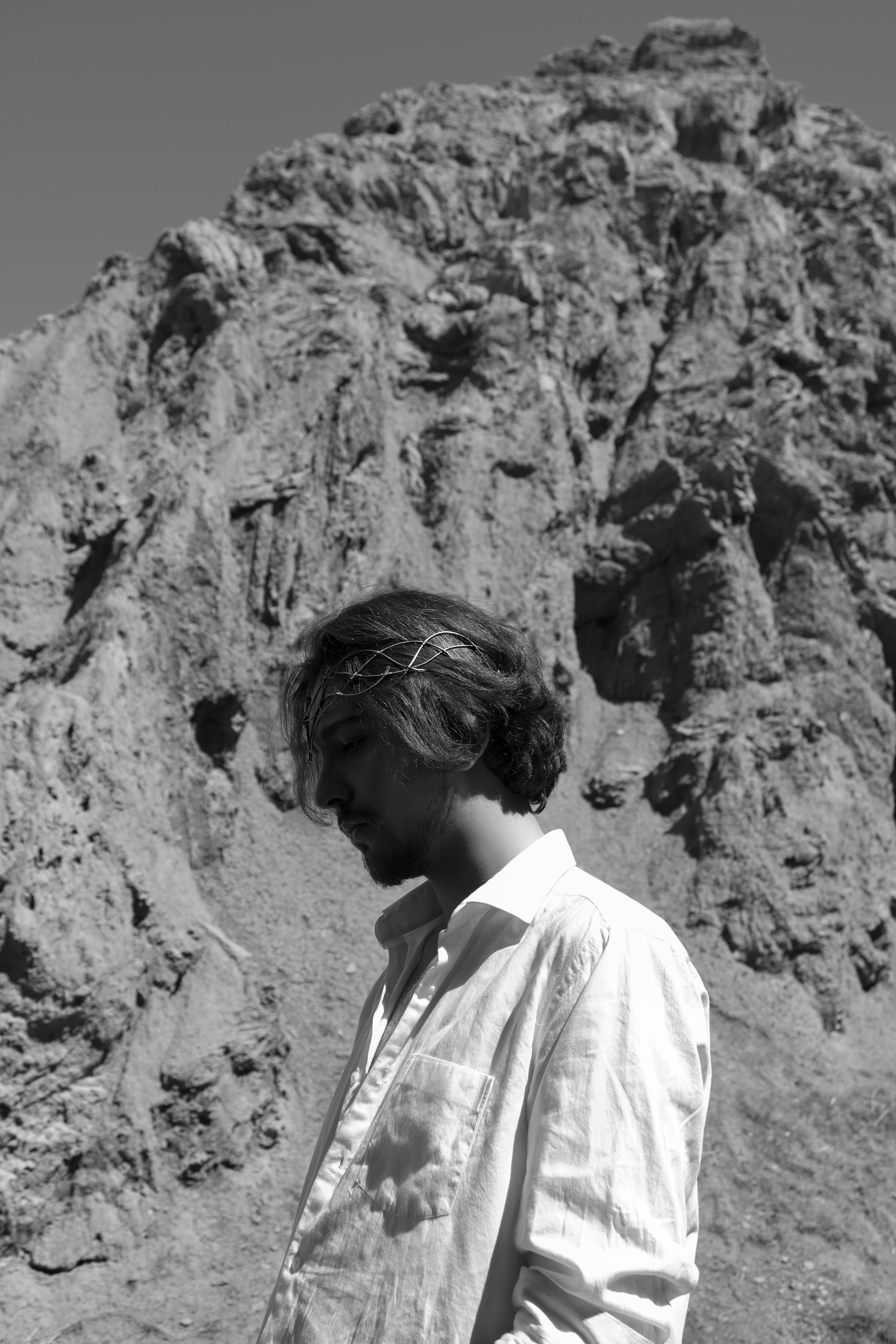 Portrait beneath a rugged cliff: quiet introspection in monochrome