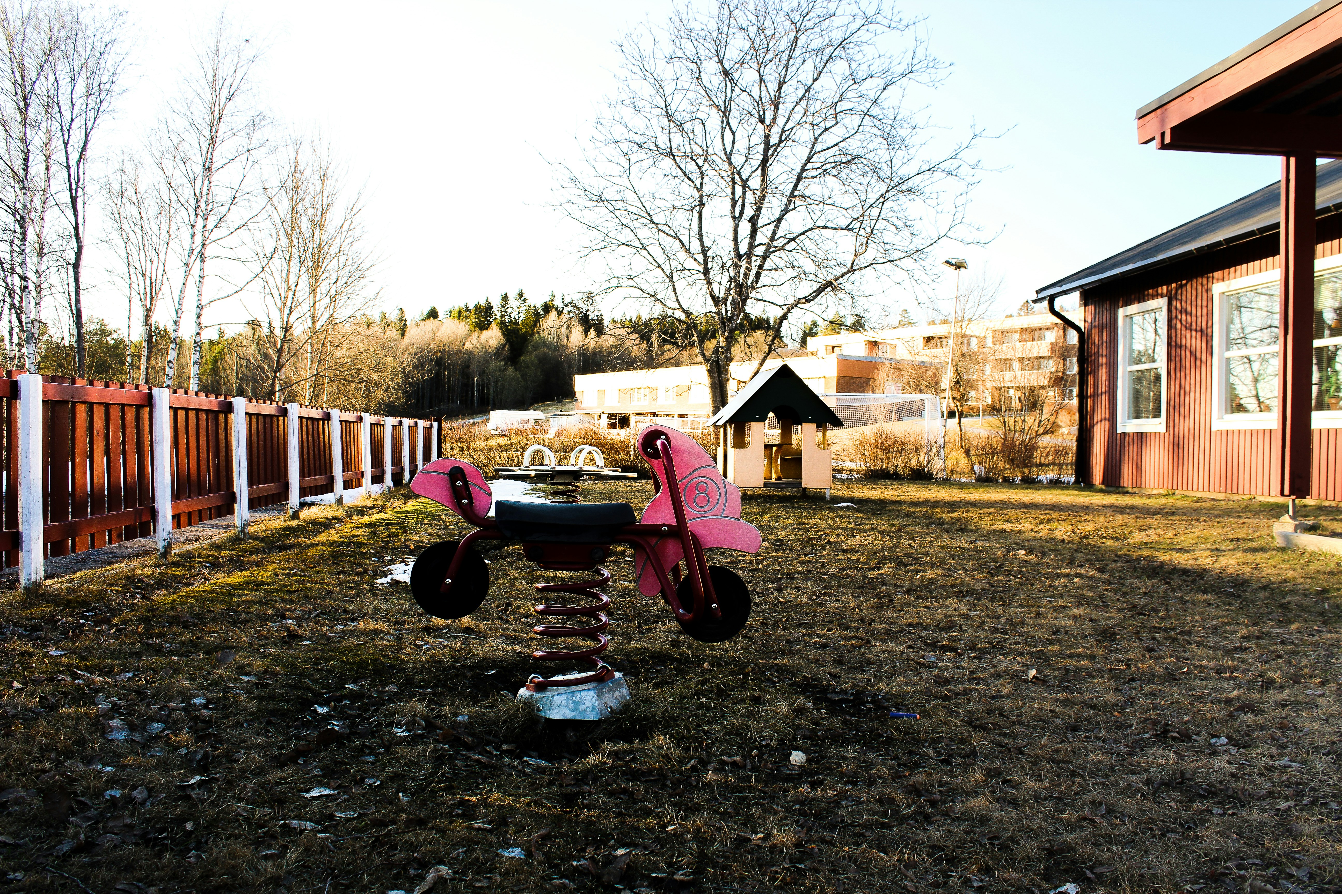 Midday Quiet: A Pink Spring Rider Anchors a Bare-Lawn Playground