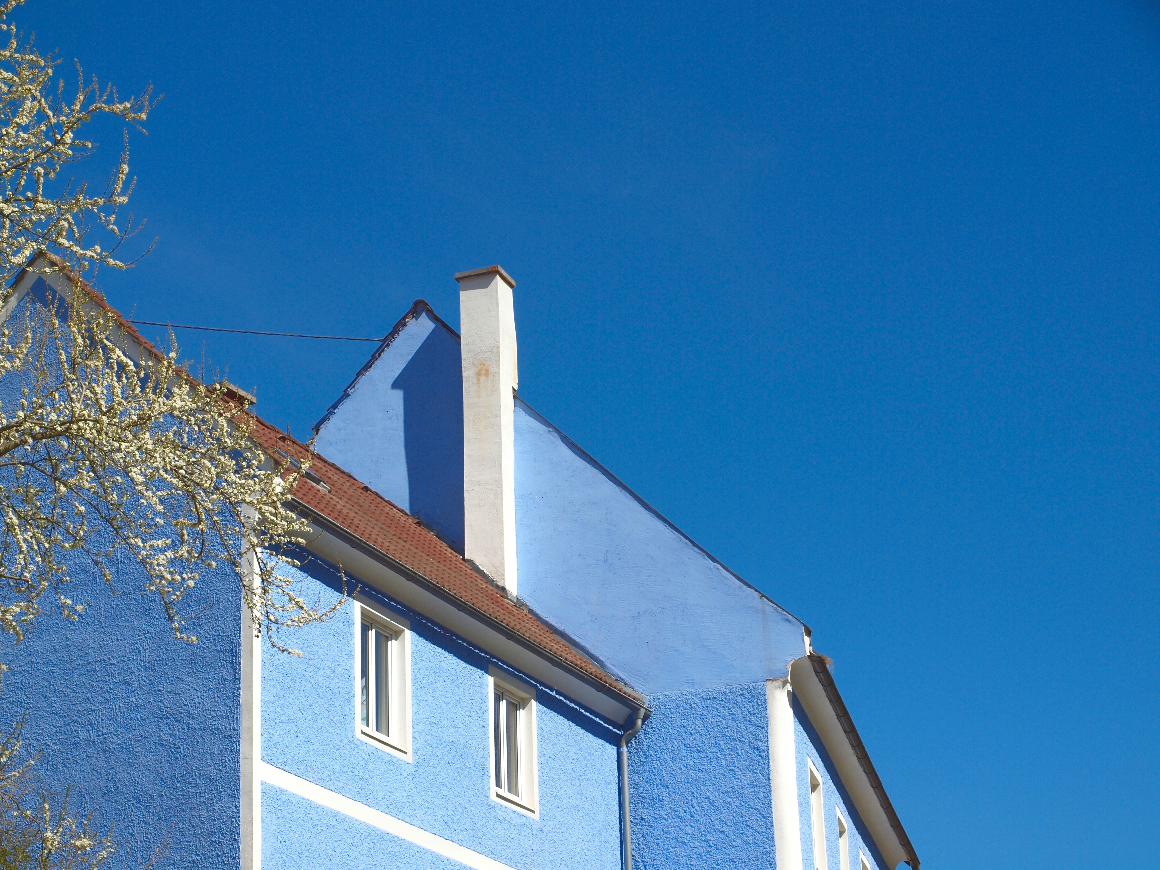 A vibrant blue house under a clear blue sky, showcasing architectural angles and details. The scene captures a tranquil moment in an urban setting.