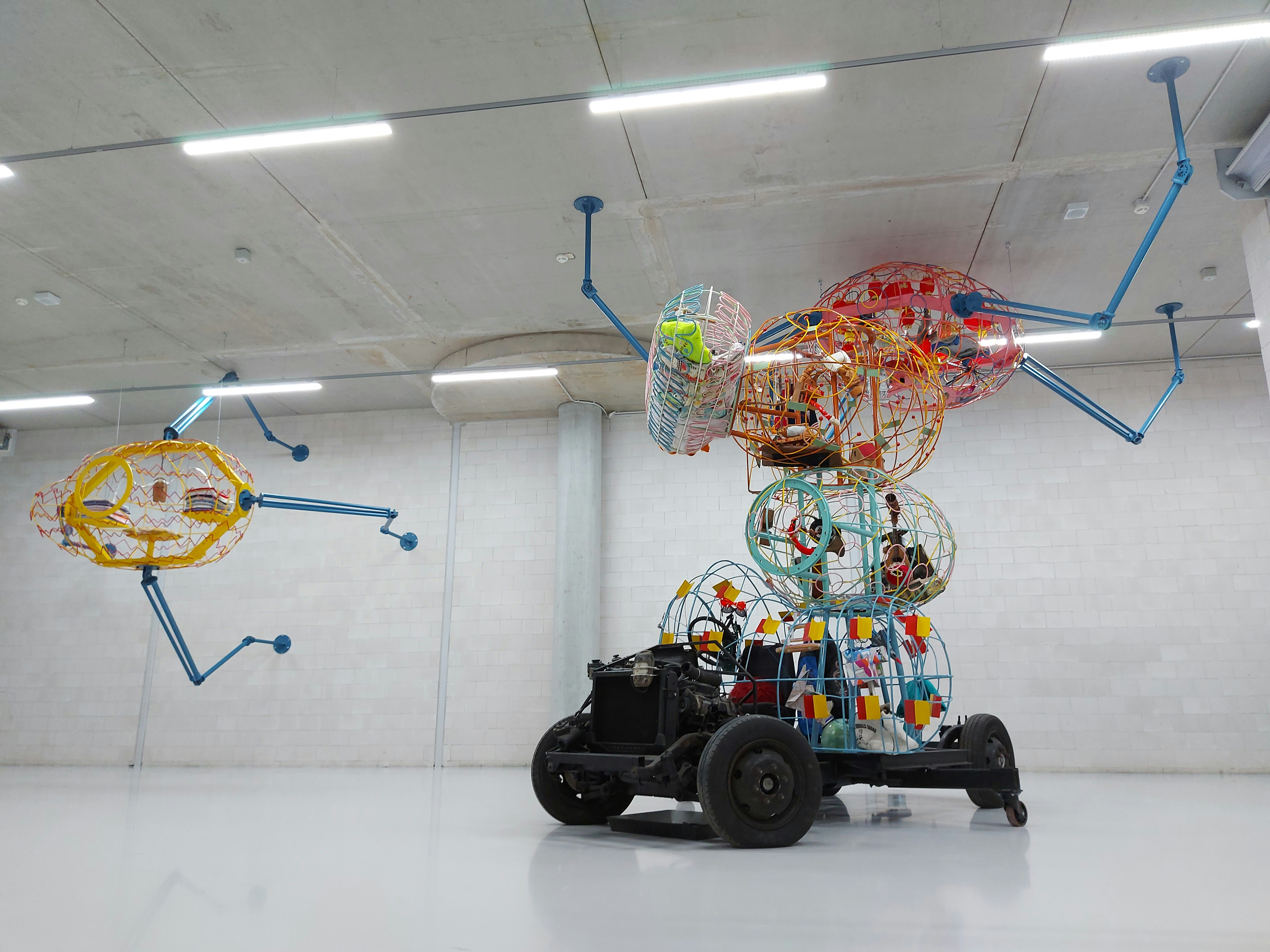 Colorful mechanical sculpture with intricate details displayed in a minimalist industrial space.