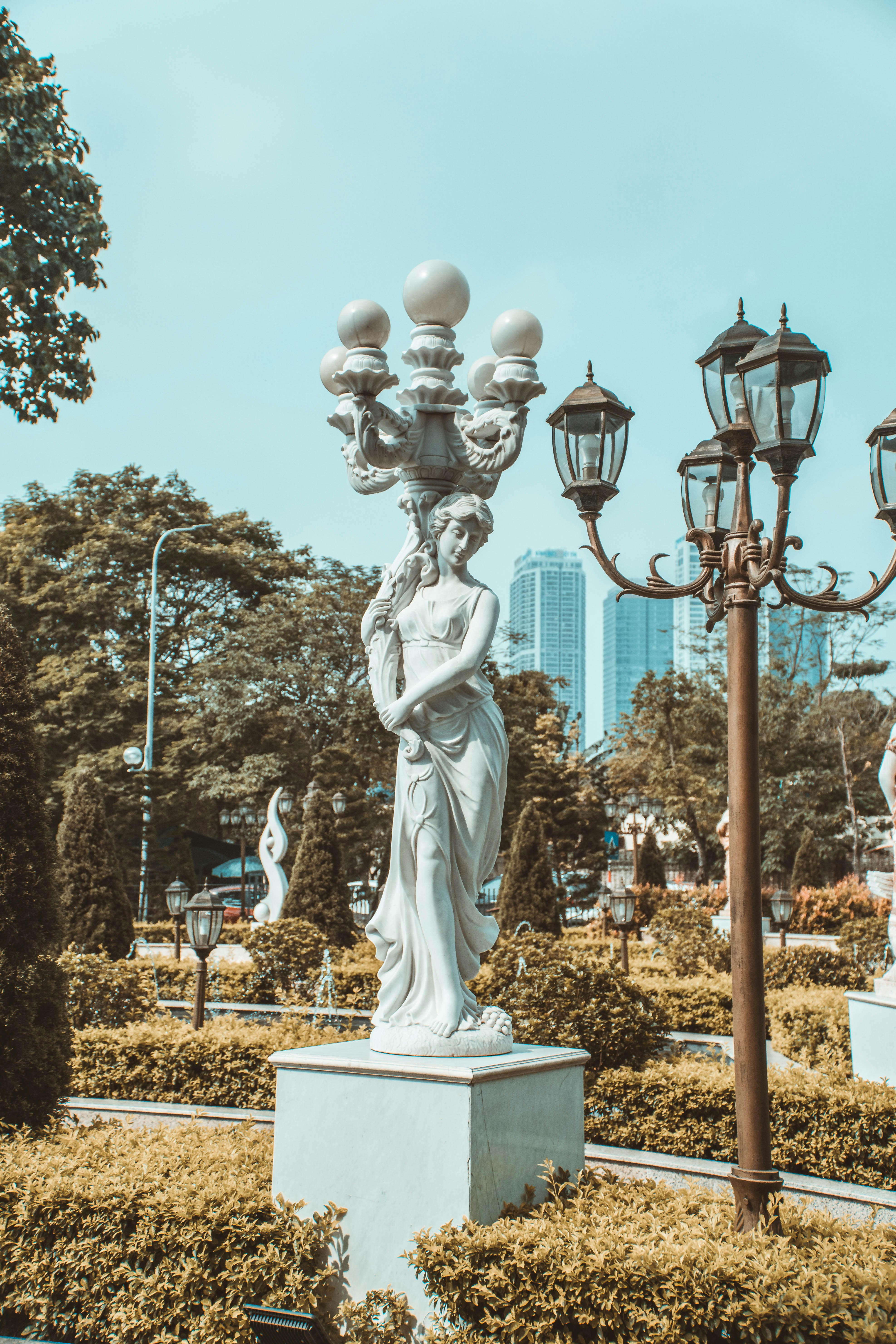Statue of Quiet Grace Surrounded by Ornate Lanterns in a Sunlit City Park
