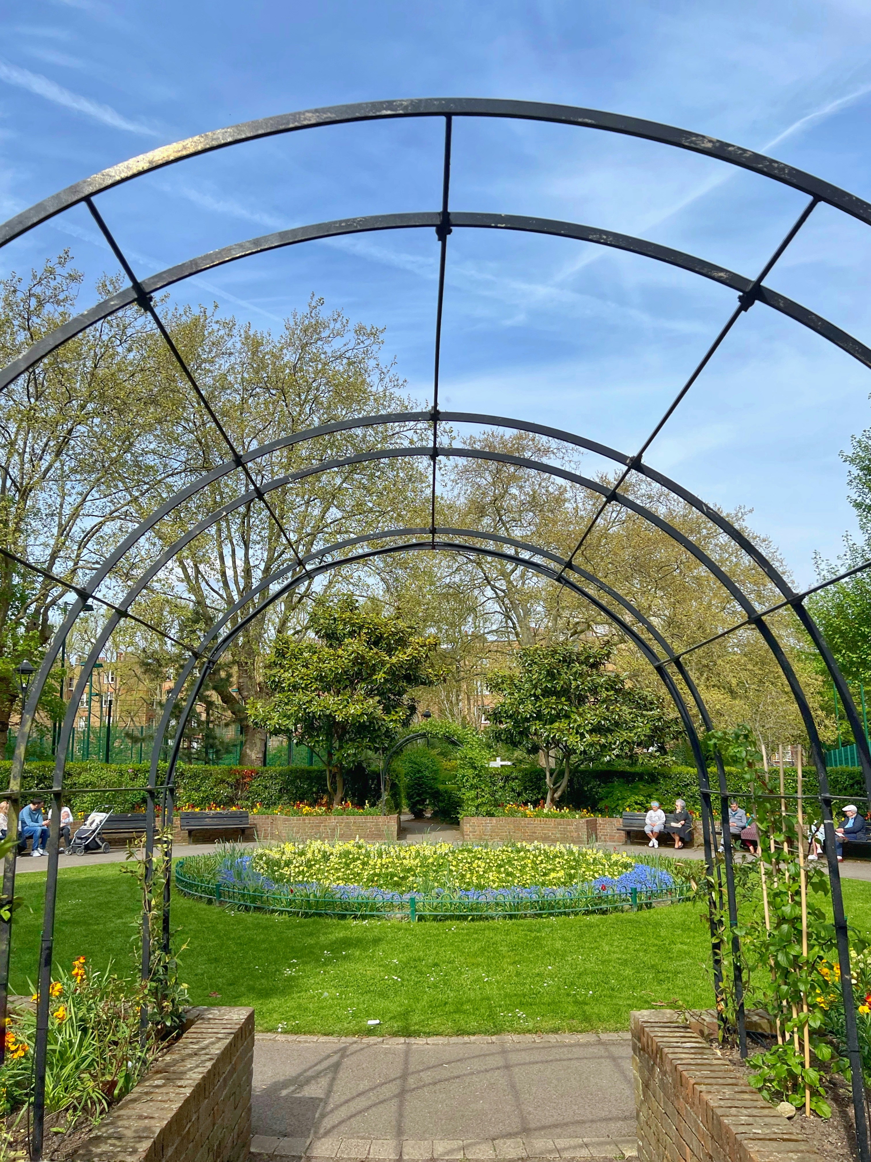 A beautifully structured archway frames a vibrant circular flower bed in a lush garden, inviting visitors to explore the serene surroundings.