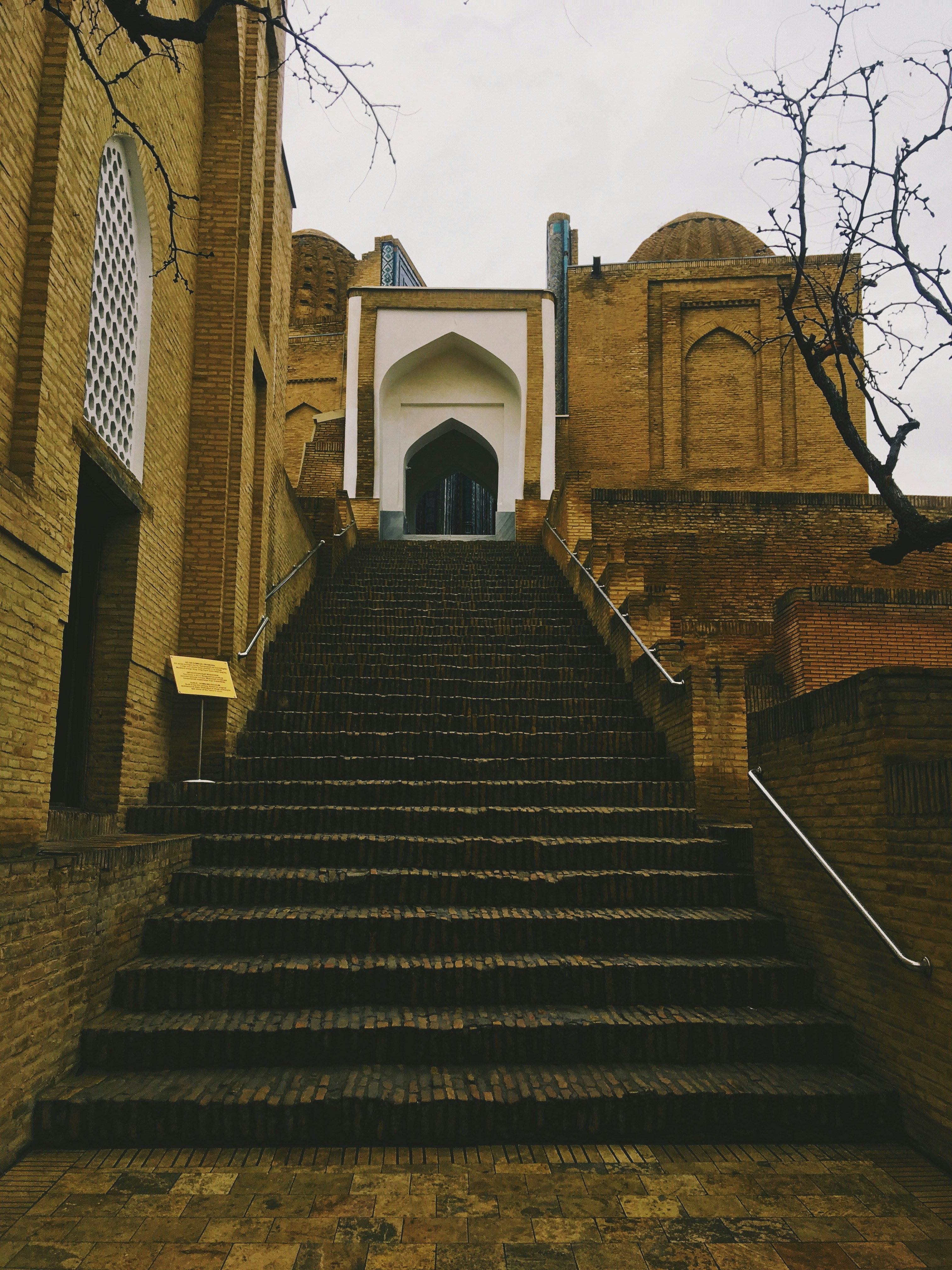 Staircase leading to an ornate archway, flanked by historical buildings and bare trees, evoking a sense of journey through time.