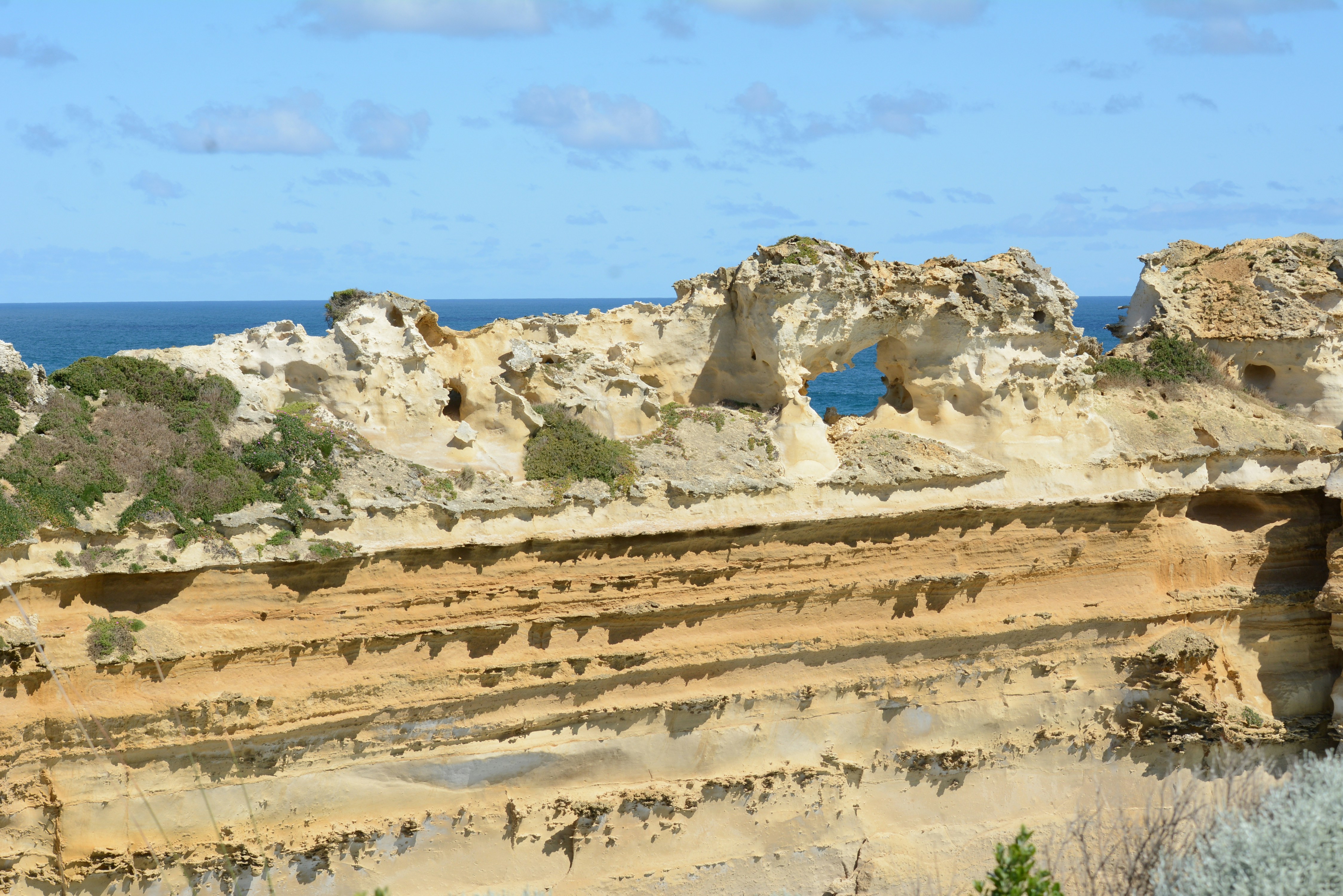 Unique rock formations with a natural arch overlooking the ocean, showcasing the intricate patterns of erosion. A vibrant coastal scene under a clear blue sky.