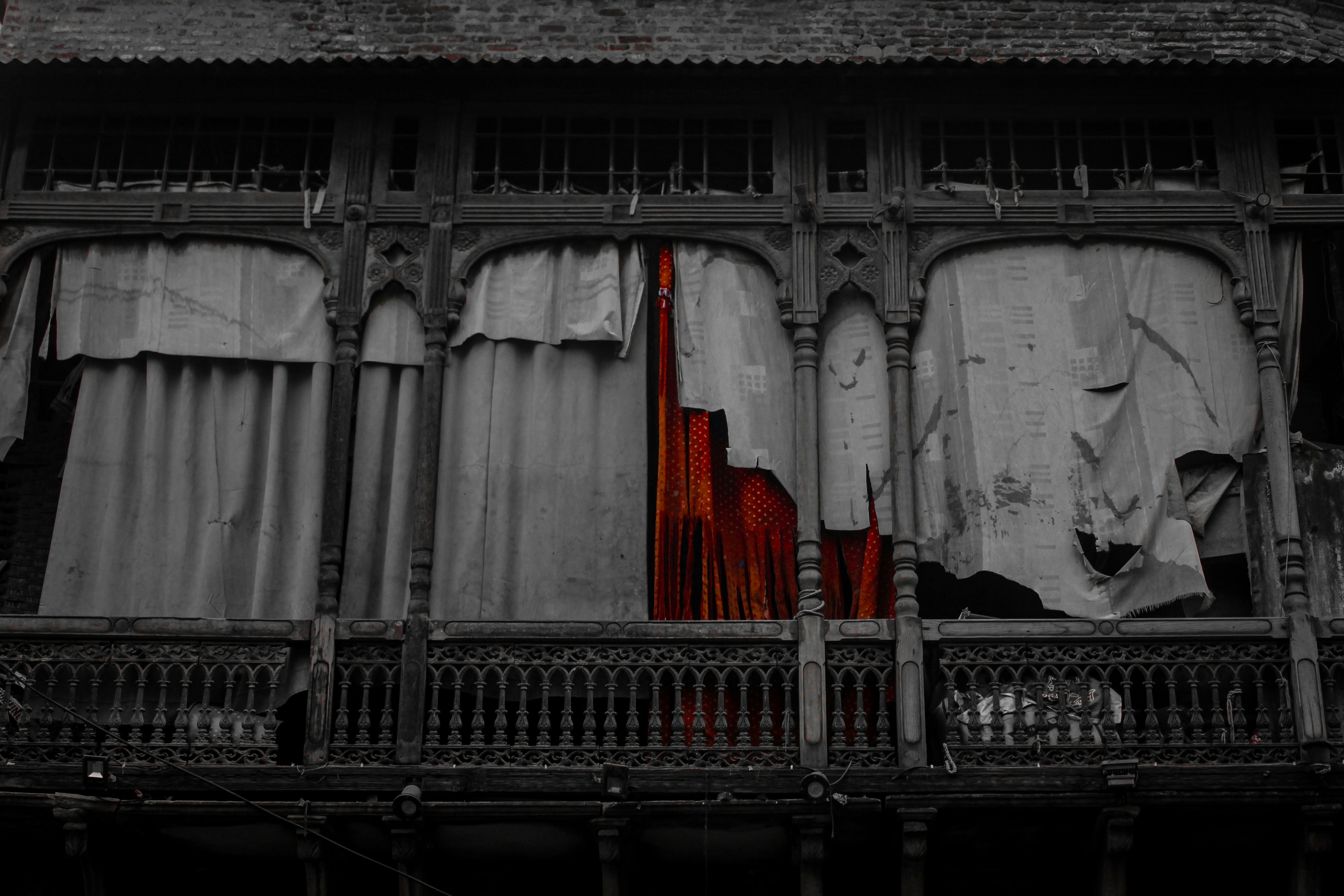A weathered balcony shrouded in tattered curtains, revealing a glimpse of vibrant red fabric behind. The scene evokes a sense of nostalgia and decay.