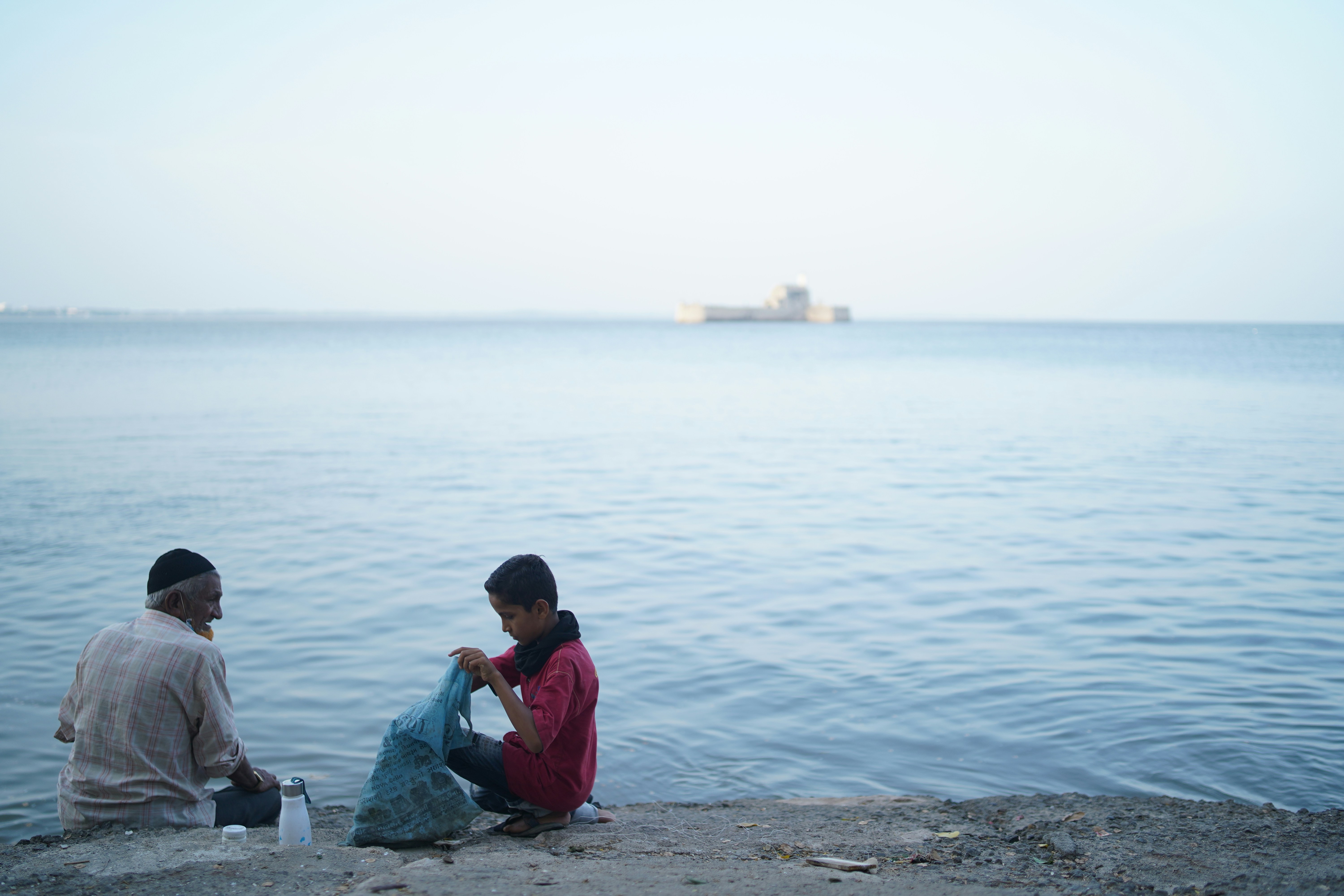 A couple of people sitting on a beach looking at the water photo – Free ...