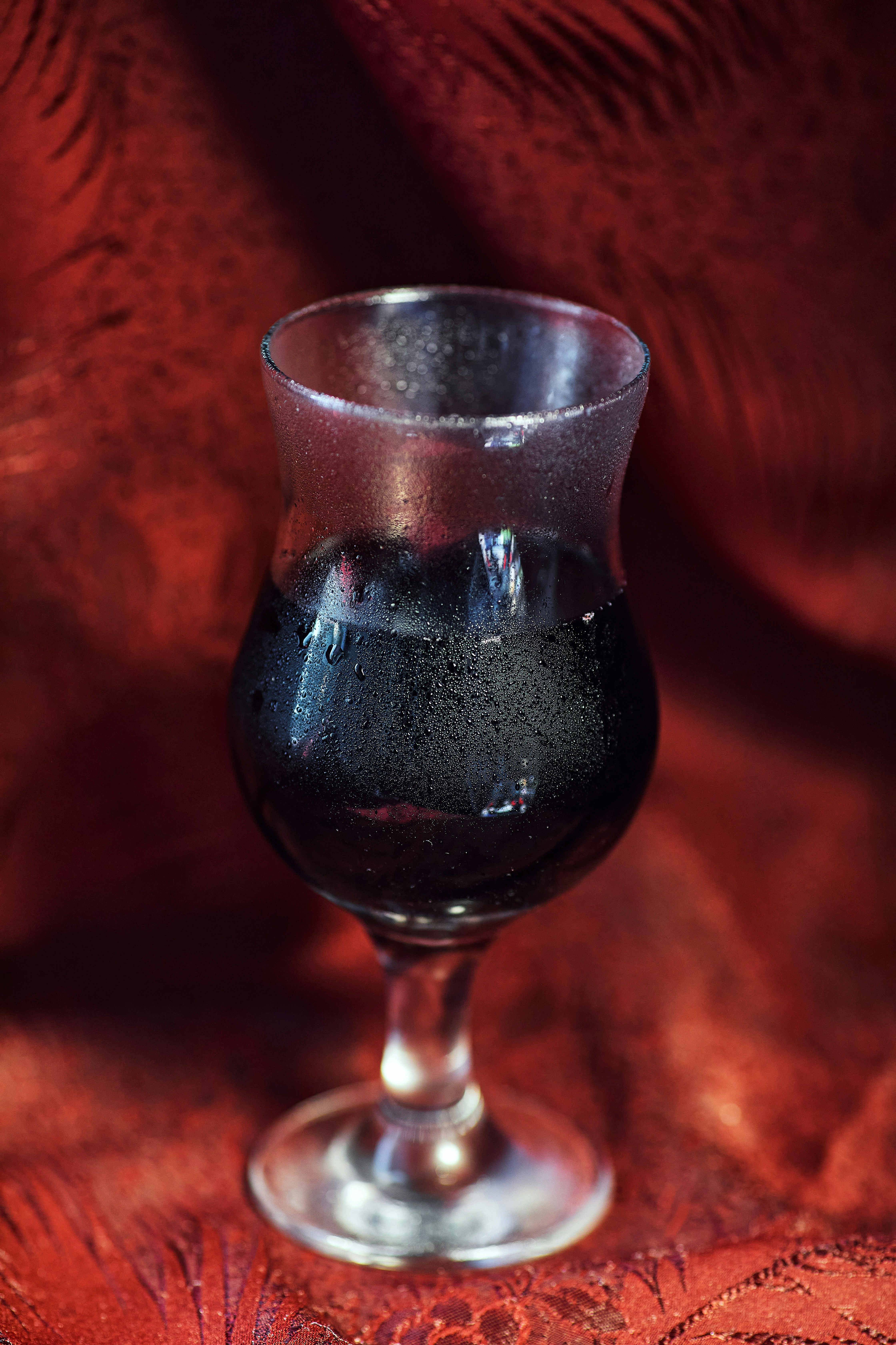 Glass of wine against a richly textured scarlet fabric background.