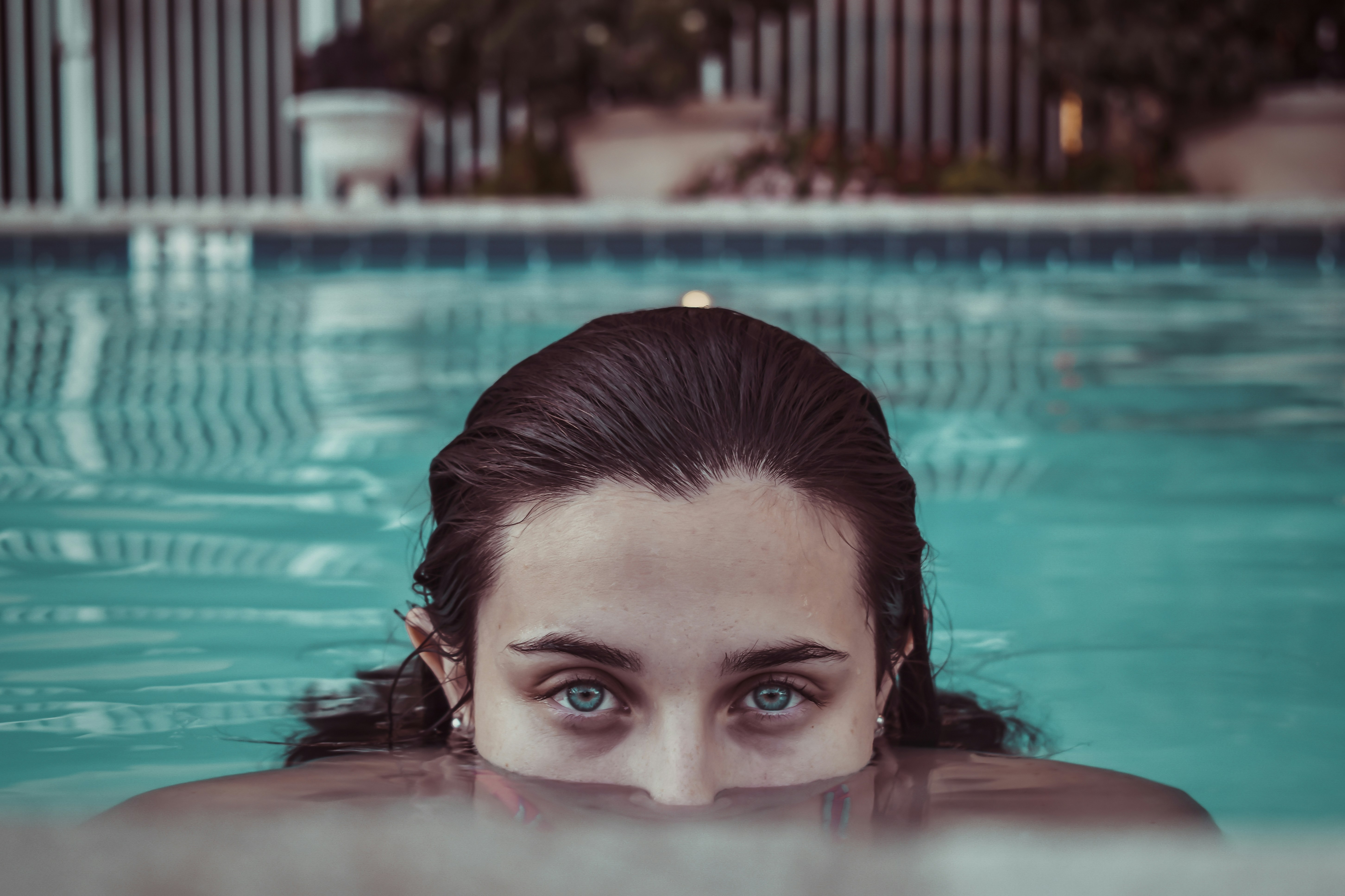 Person with blue eyes partially submerged in a pool, focusing intently.