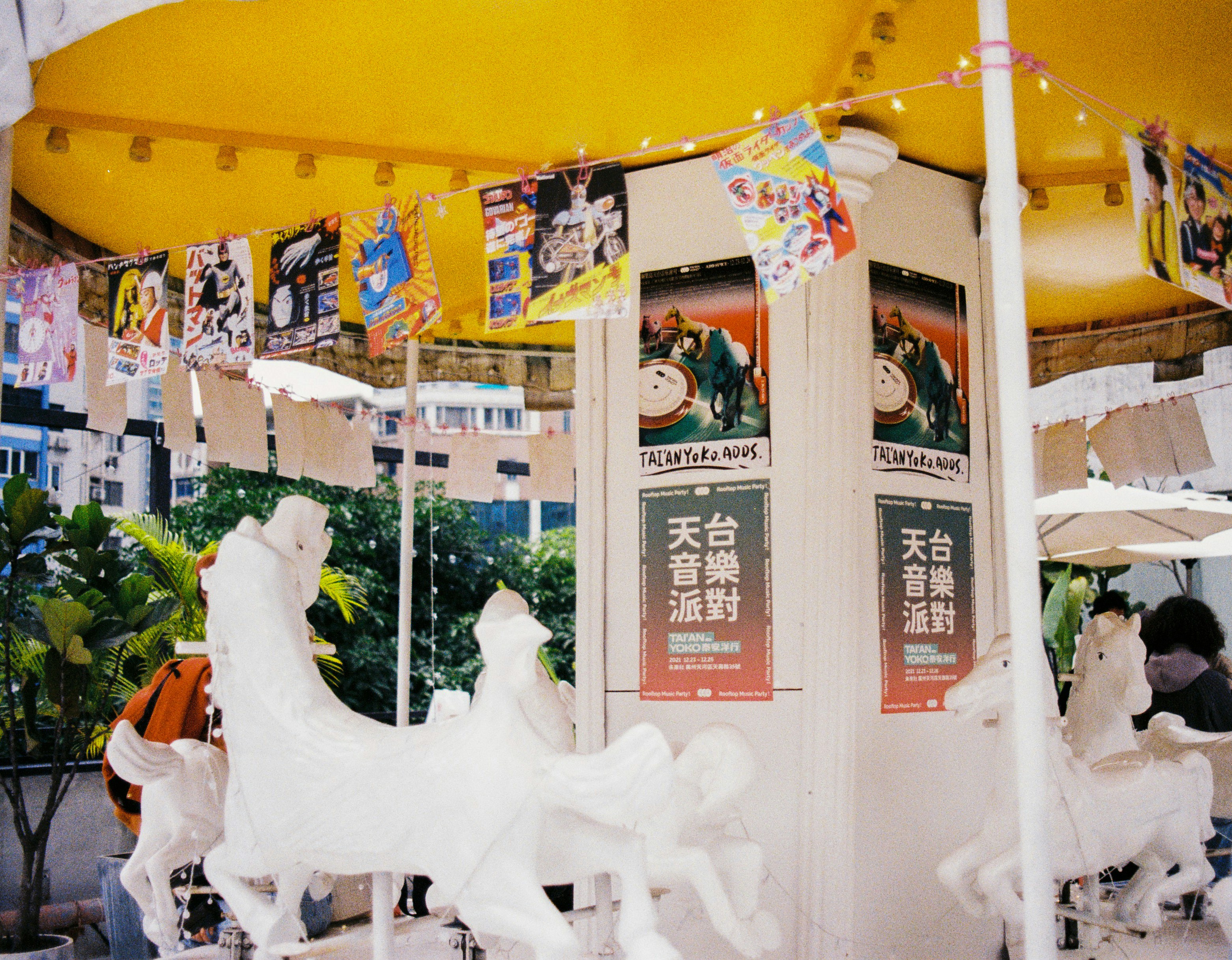 A vibrant carousel adorned with colorful banners and playful horse figures, set against a lively backdrop of greenery and urban life.