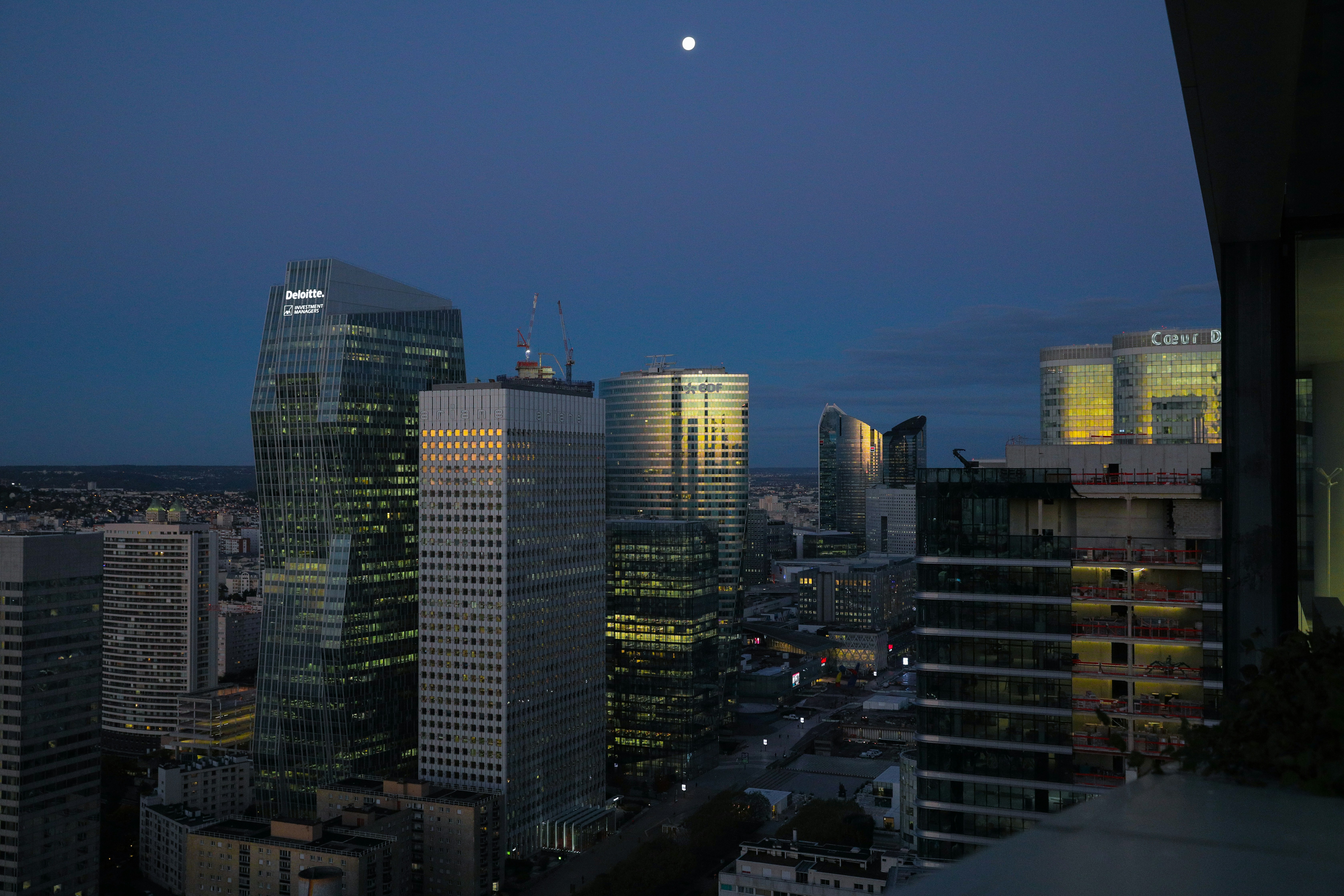 Moon rising over a modern city skyline with illuminated skyscrapers at dusk.