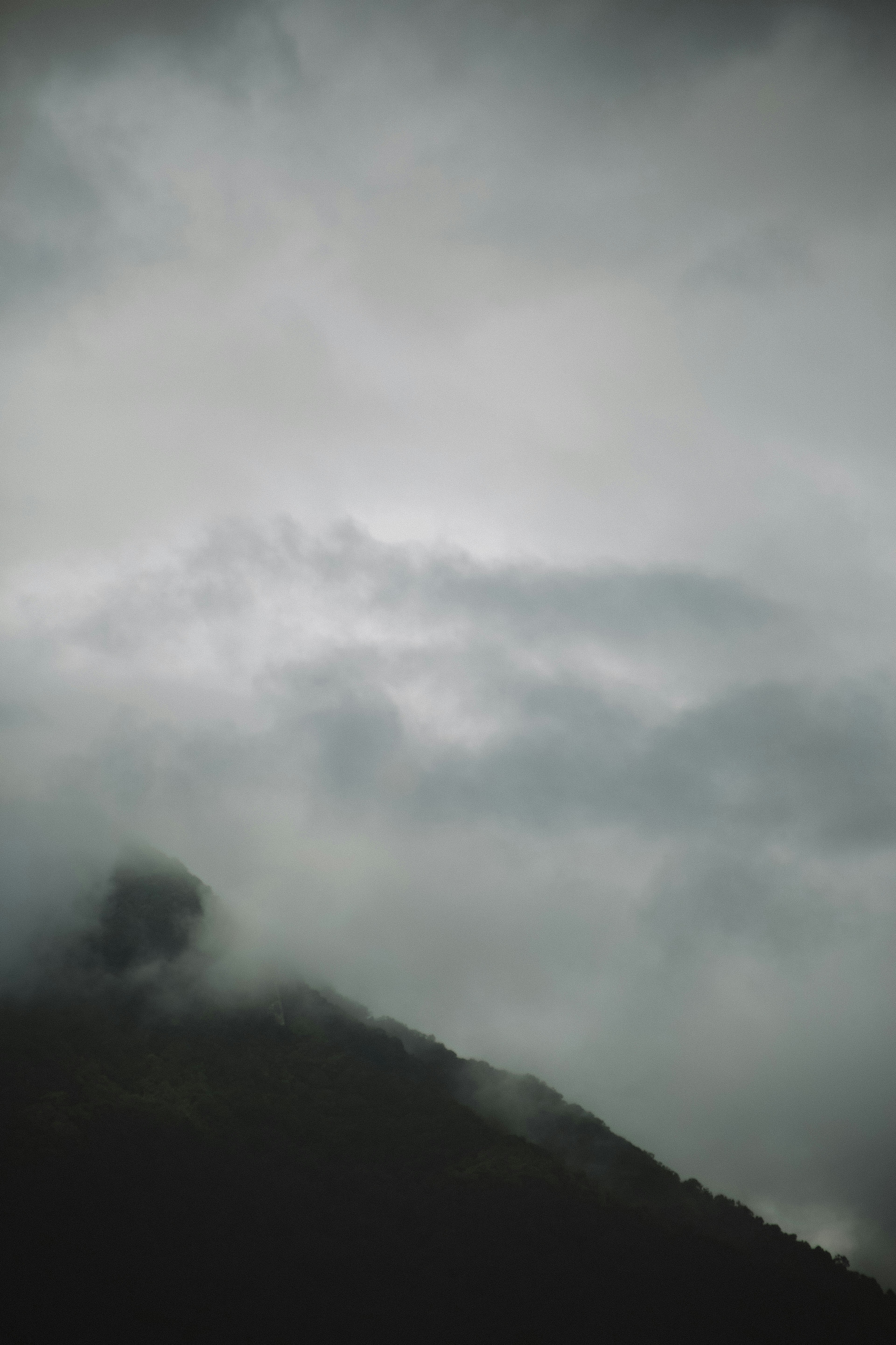 Clouds envelop a dark, silhouetted mountain peak under a moody, overcast sky.