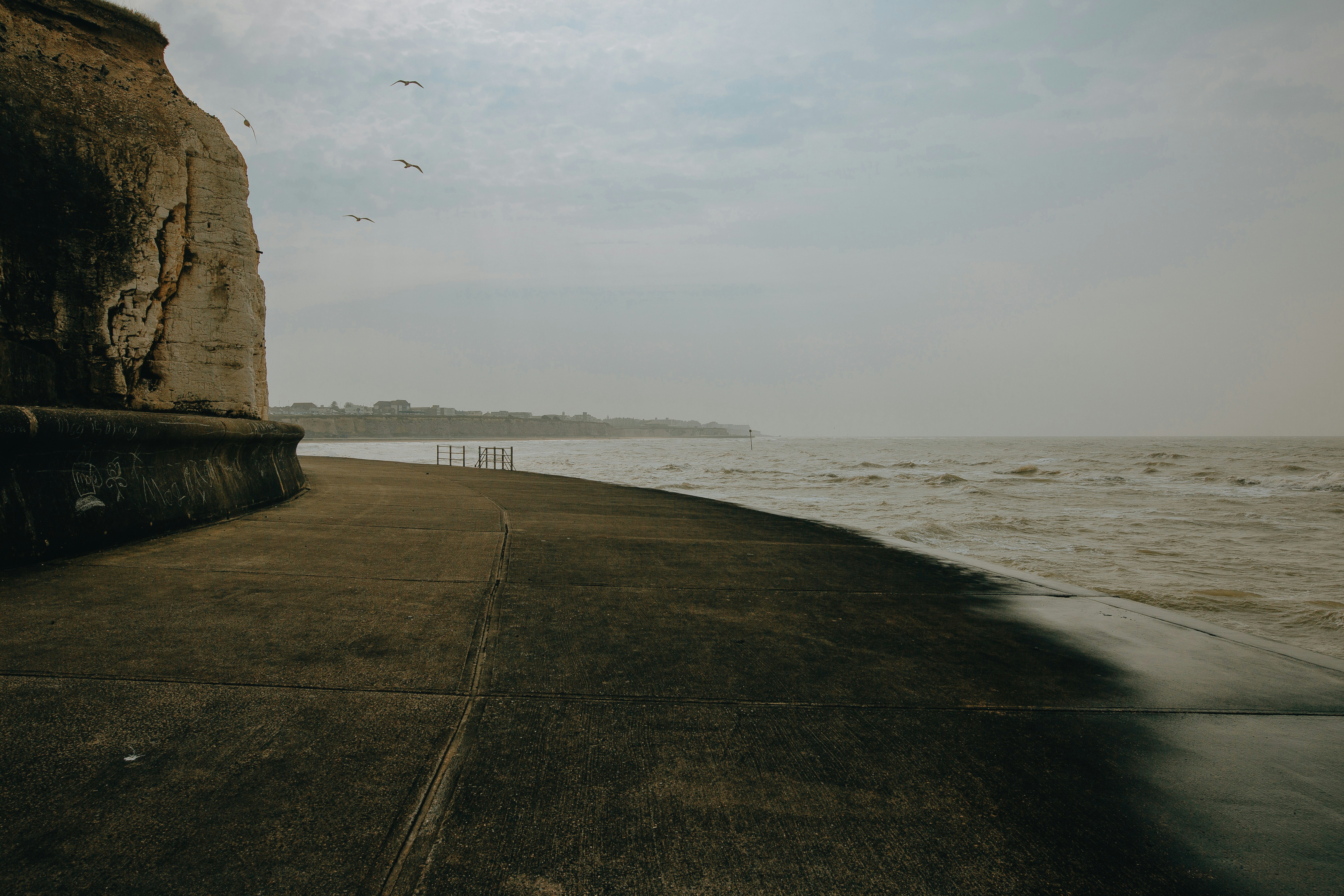 Expansive shoreline with rugged cliffs and a calm sea under a cloudy sky.