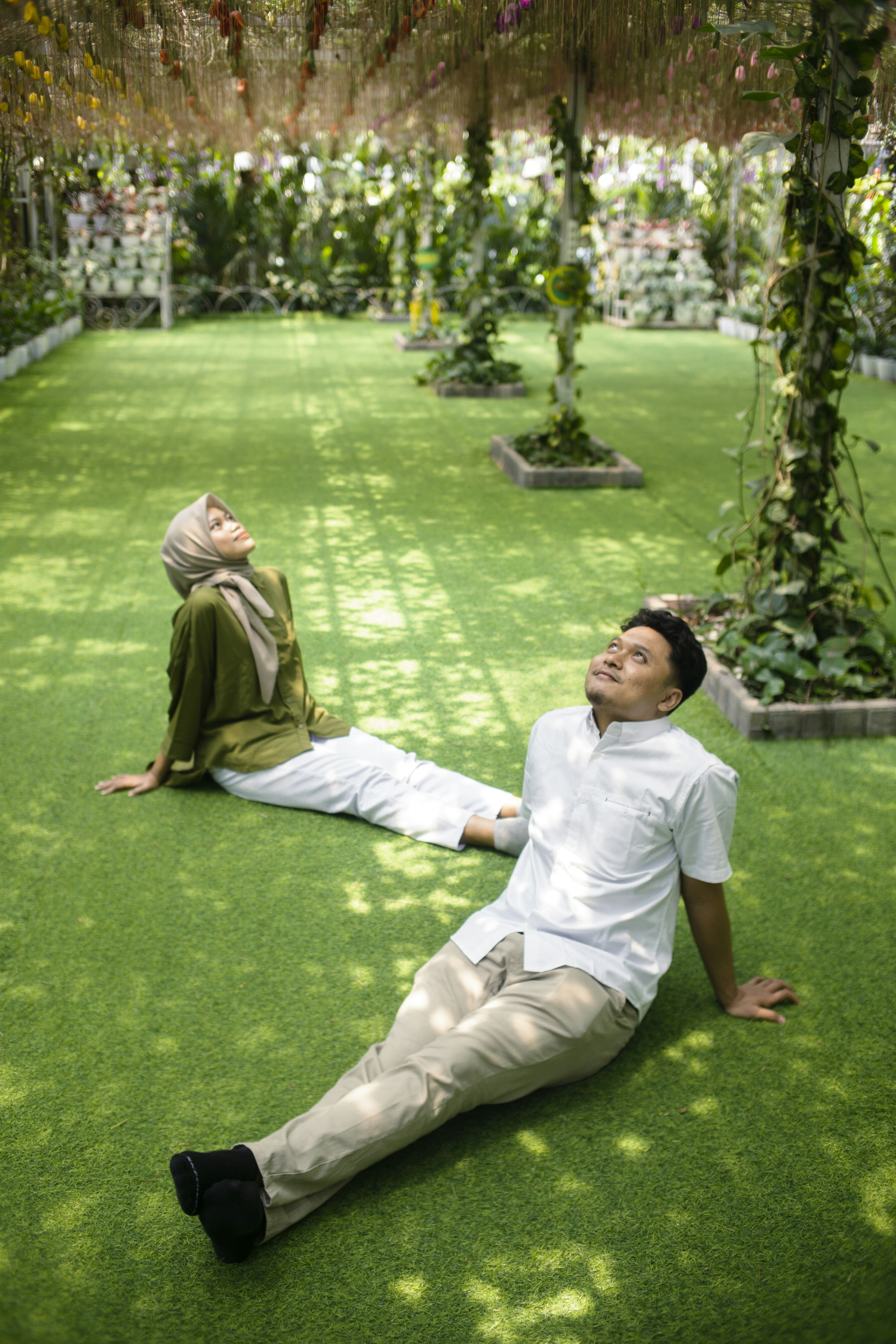 Two individuals relax on a lush green lawn beneath a canopy of flowers, embodying tranquility and connection with nature.