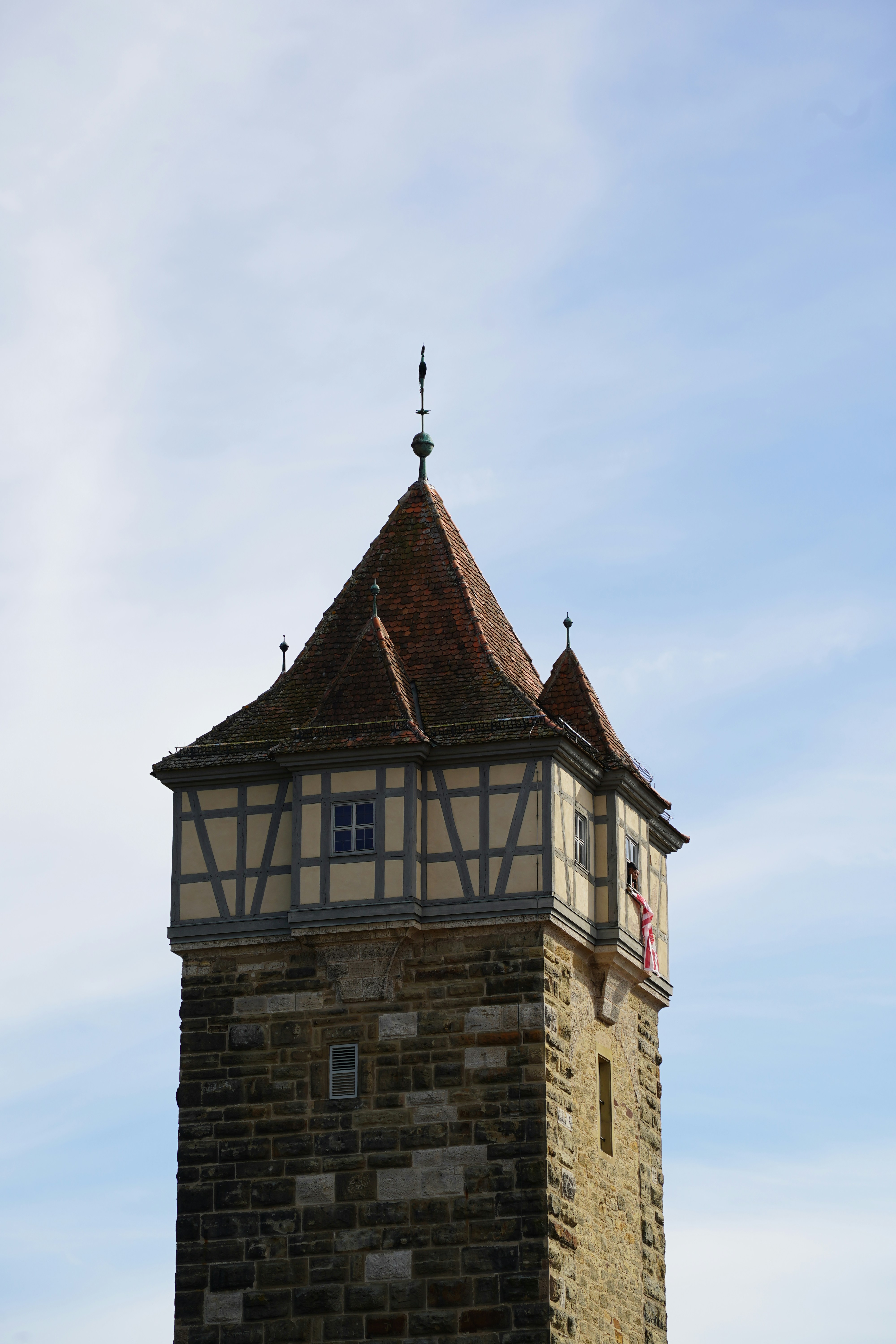 Historic tower featuring a distinctive peaked roof and wooden framework against a bright blue sky.