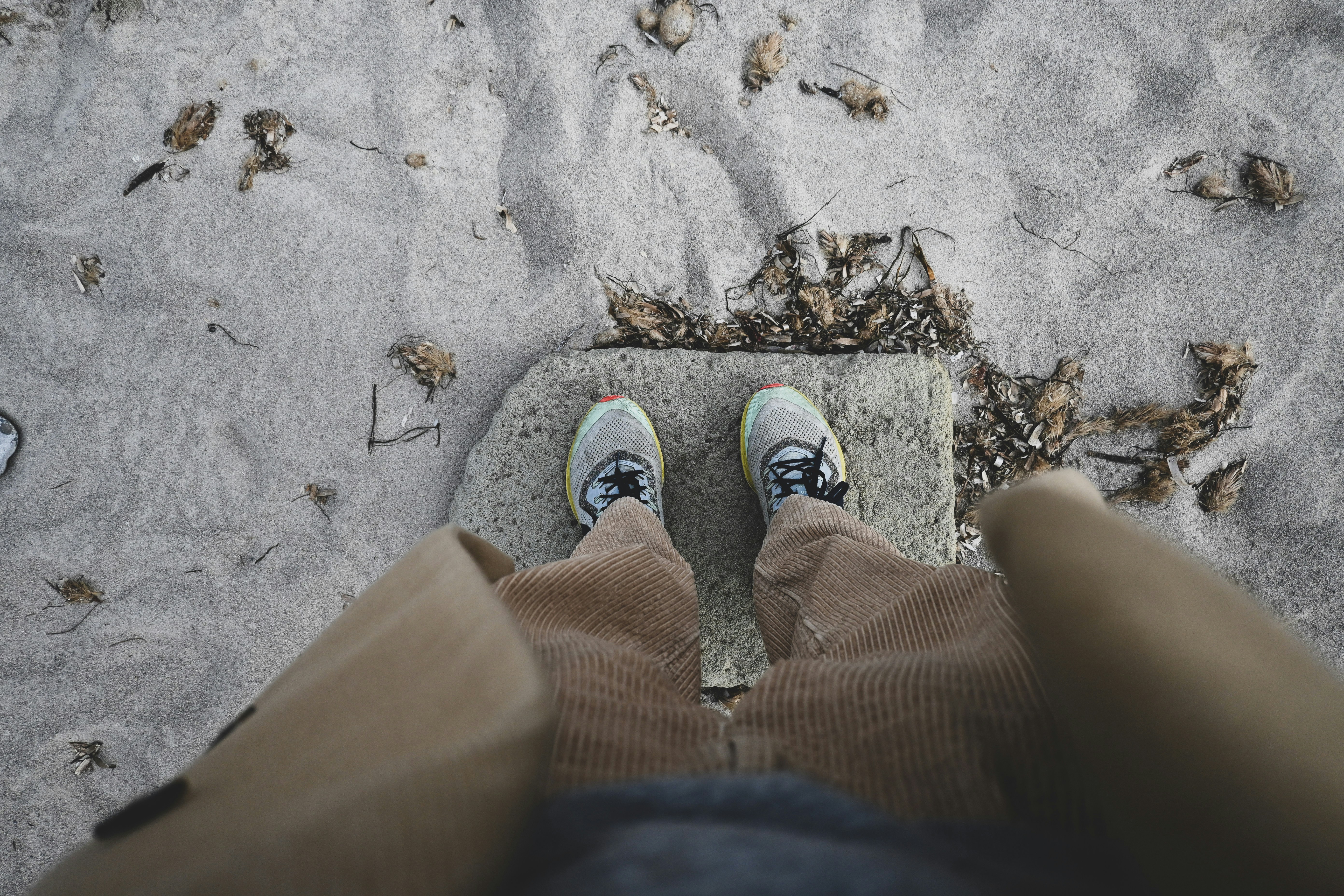 Feet standing on a stone slab surrounded by sandy terrain and scattered leaves.