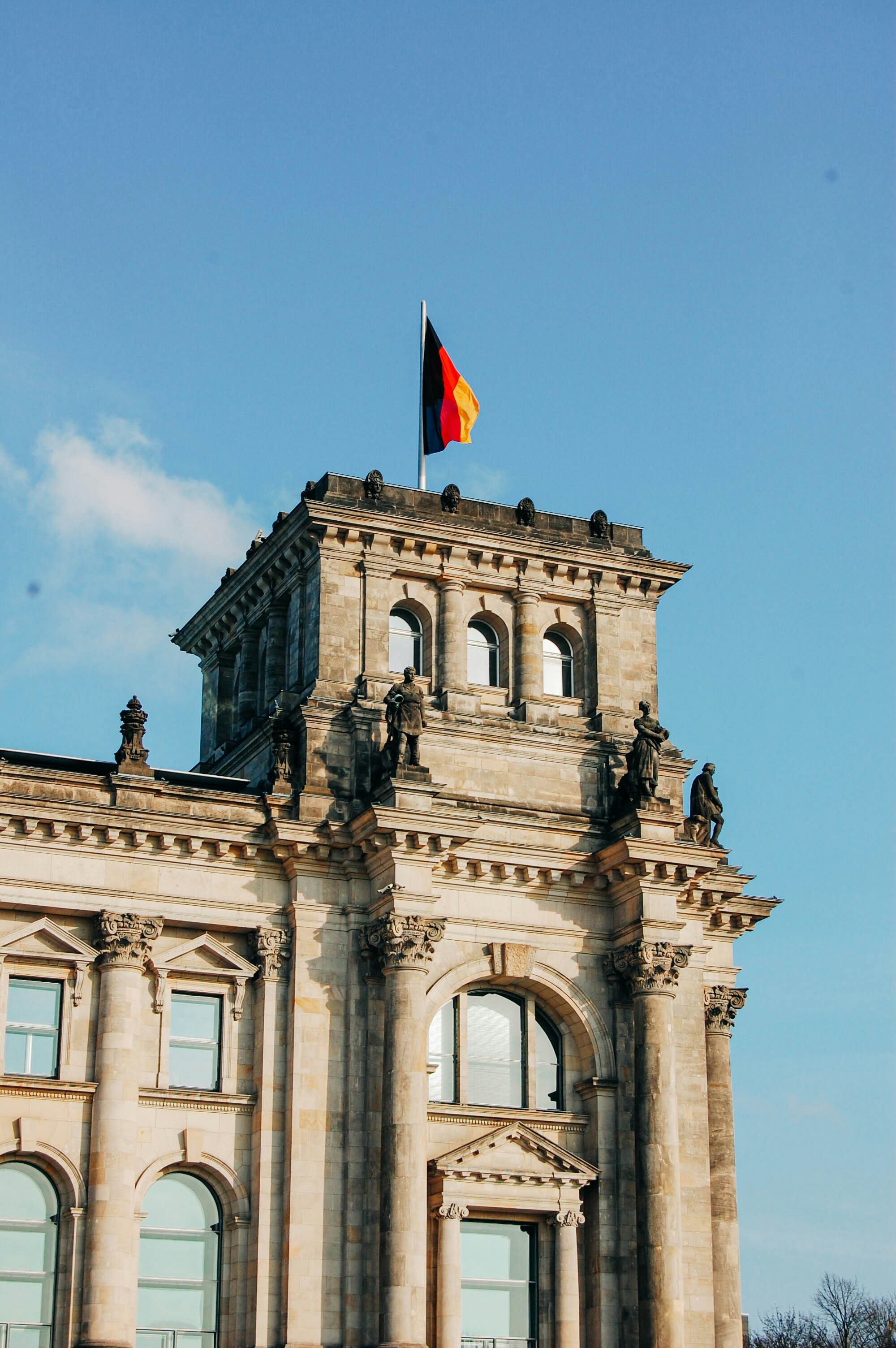 German flag proudly waving atop a historic government building under a clear blue sky.
