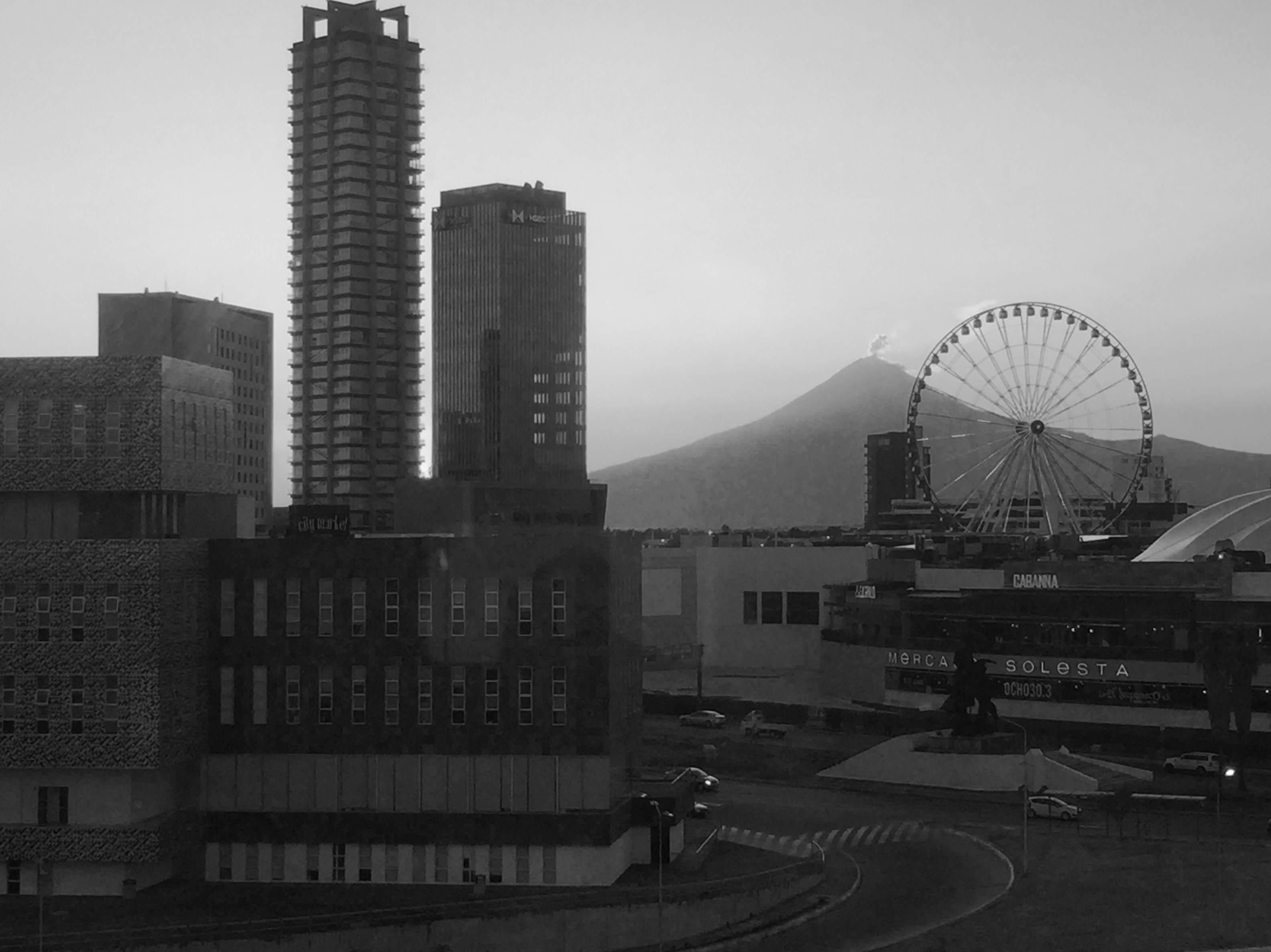 City skyline with tall buildings and a ferris wheel, set against the backdrop of a smoking volcano.