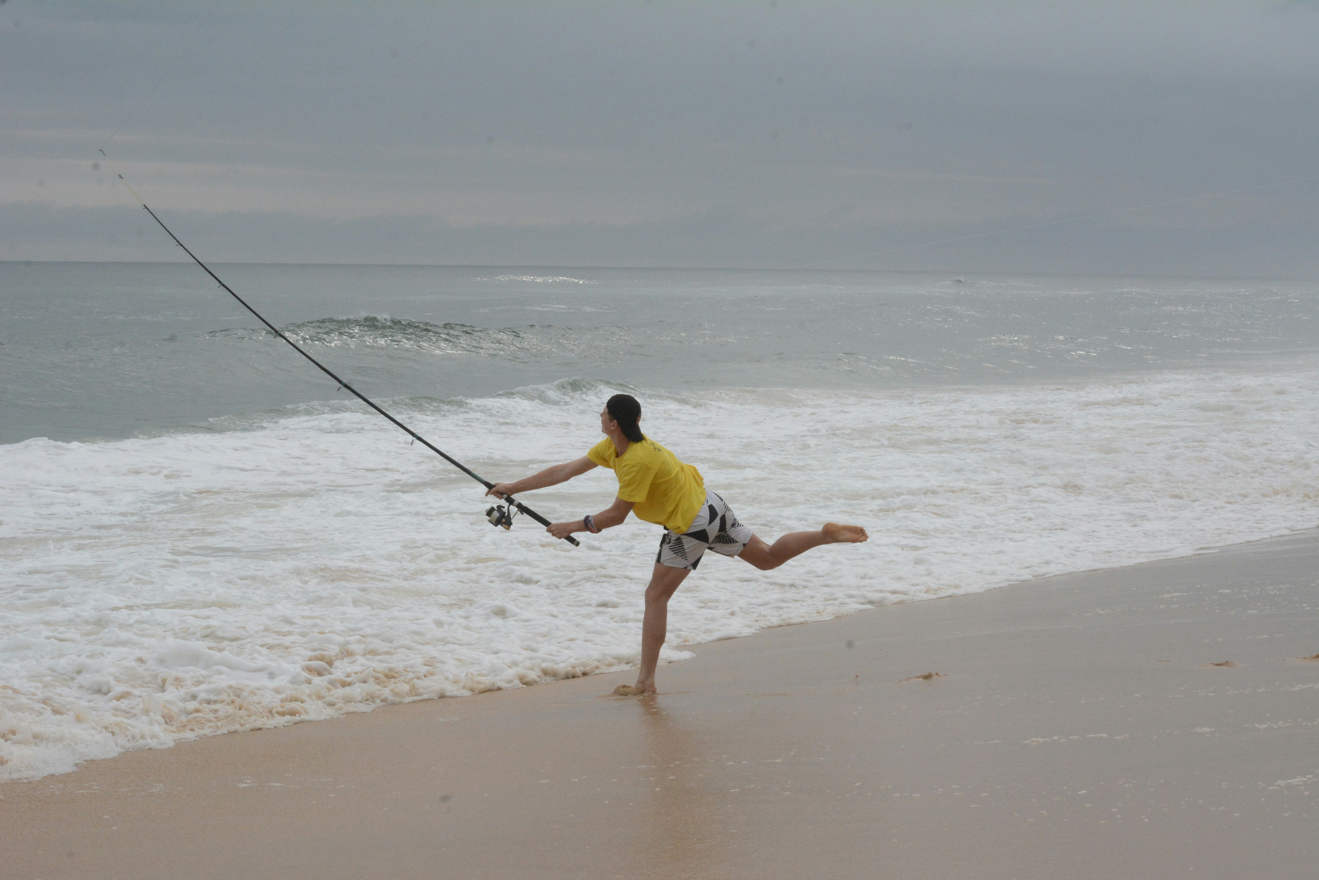 Midair Cast at the Shore: A Lone Angler in Full Extension