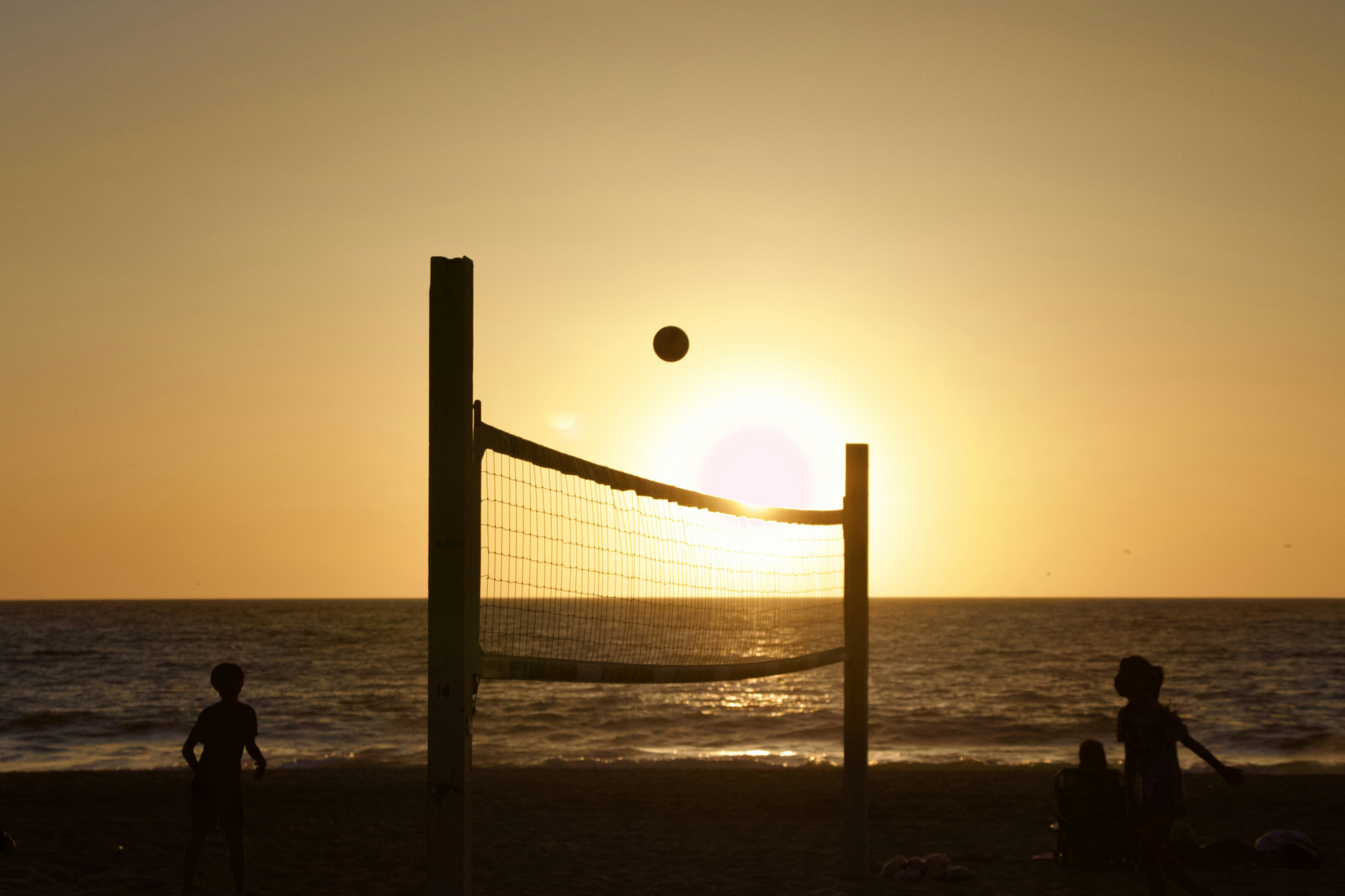 Silhouetted beach volleyball game against a vibrant sunset over the ocean.