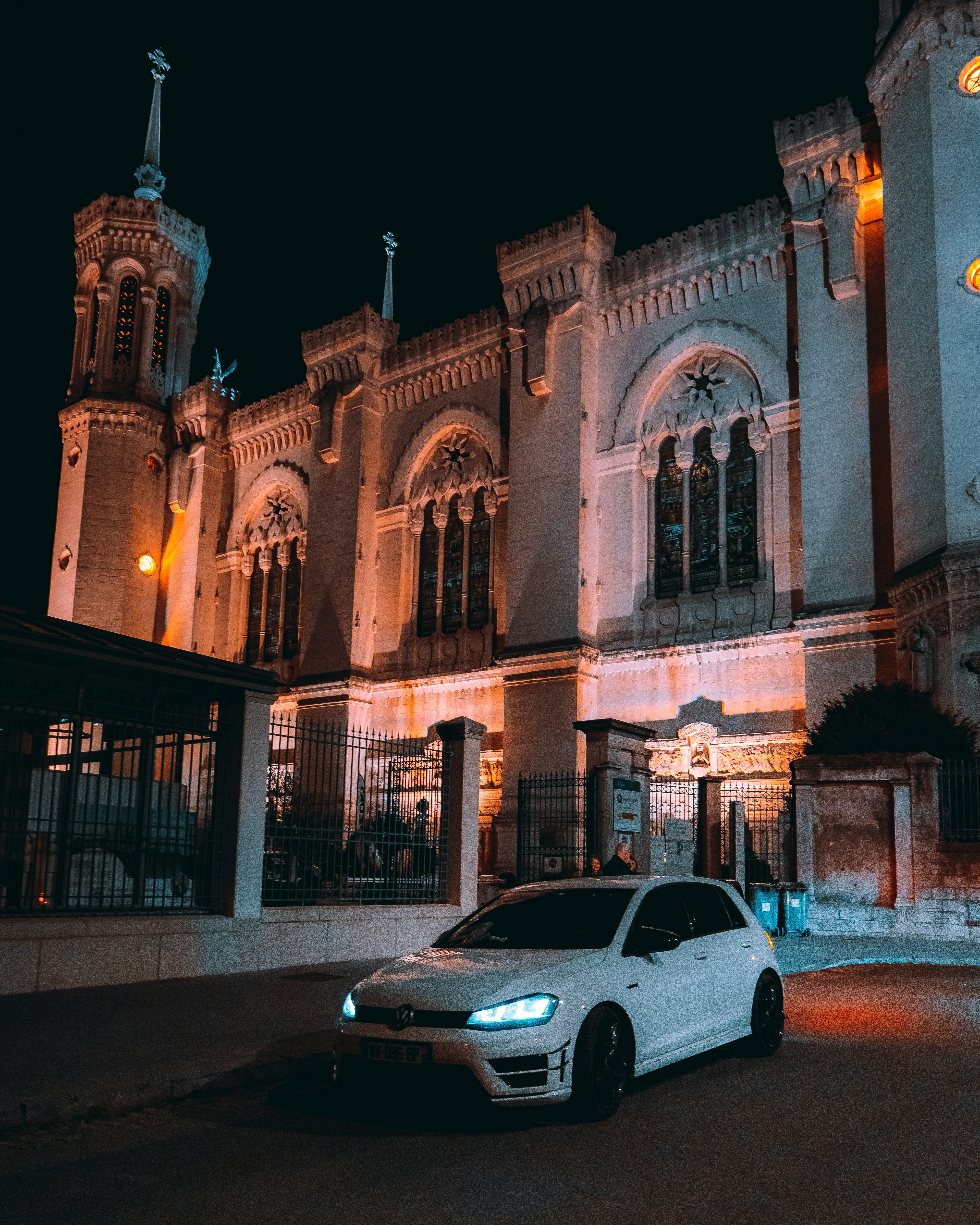 Midnight White Hatchback at the Foot of an Amber-Lit Gothic Facade