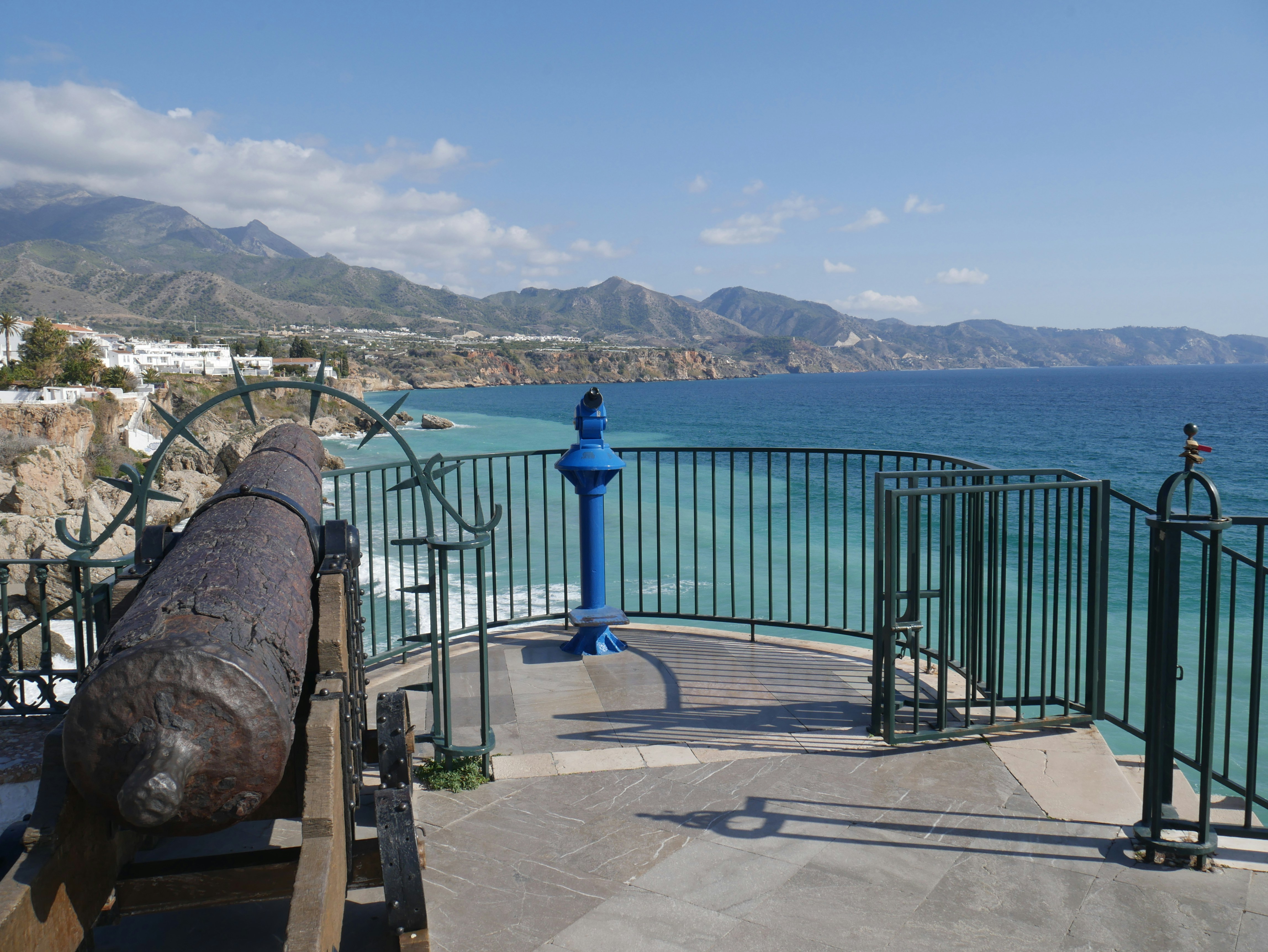 Historic cannon overlooking a vibrant blue coastline framed by mountains under a clear sky.