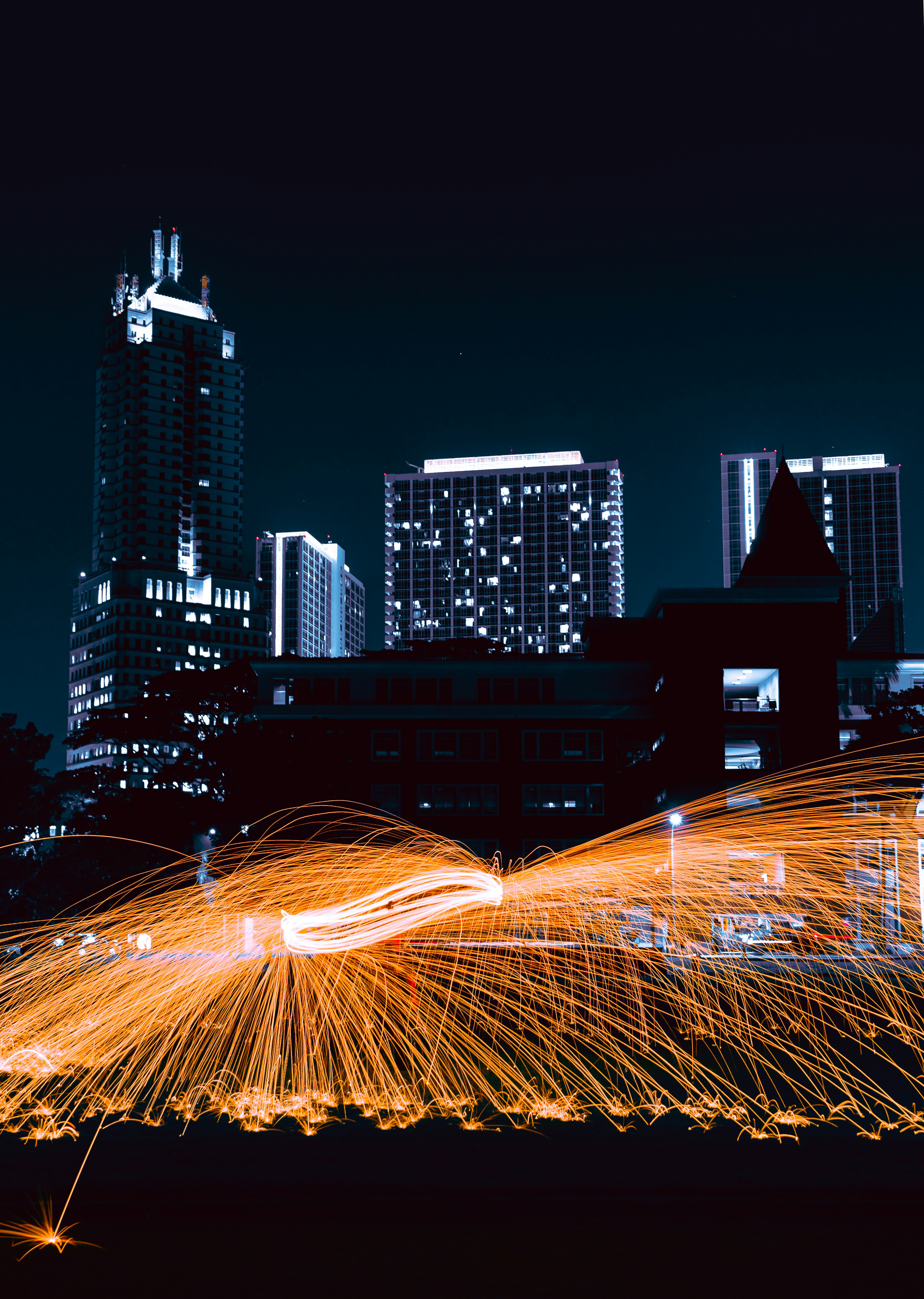 Vibrant light trails weave through a cityscape, highlighting towering skyscrapers against a night sky. The dynamic contrast emphasizes urban energy.