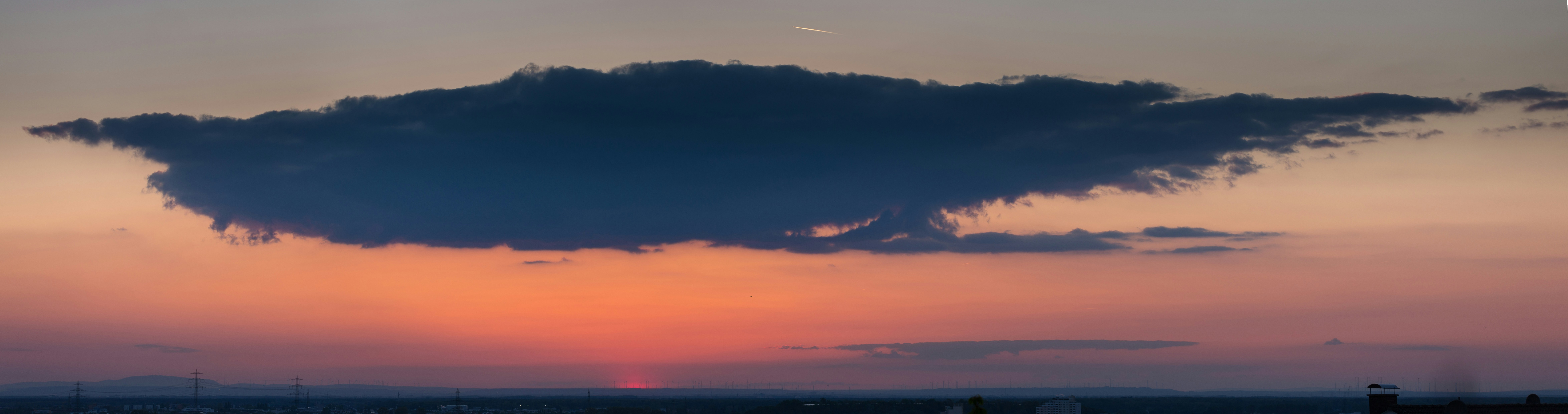 A dramatic cloud formation silhouetted against a vibrant sunset, blending hues of orange and blue. The scene captures the transition from day to night.
