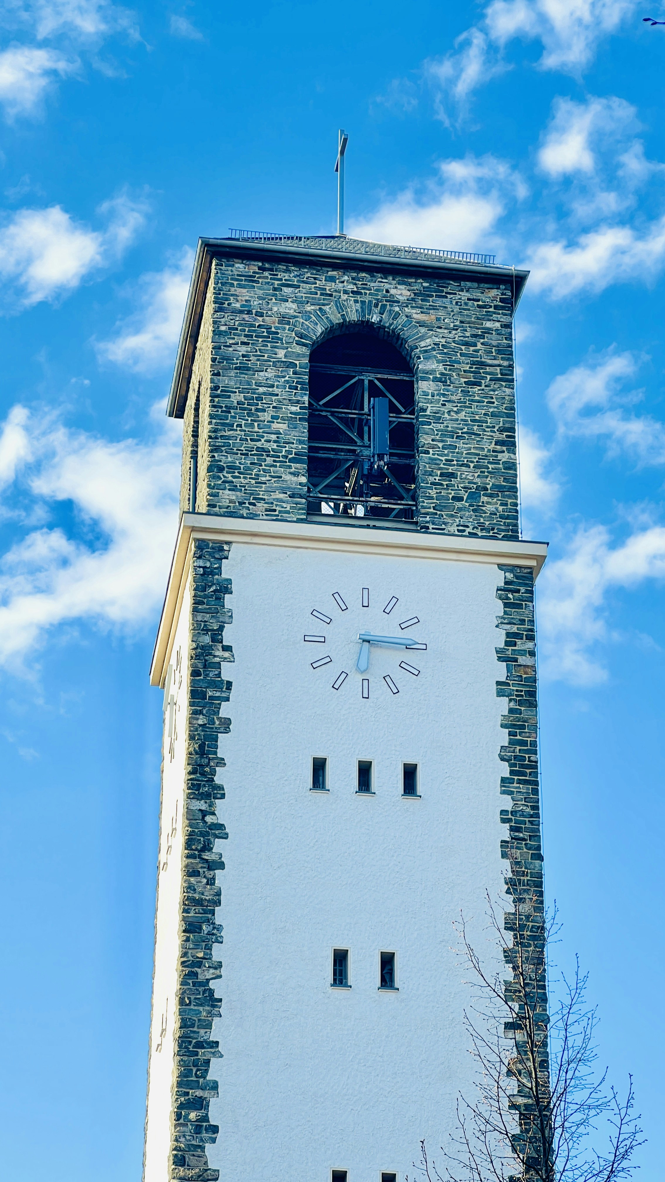 Historic clock tower rising against a bright blue sky with wispy clouds, showcasing its intricate stonework and clock face.