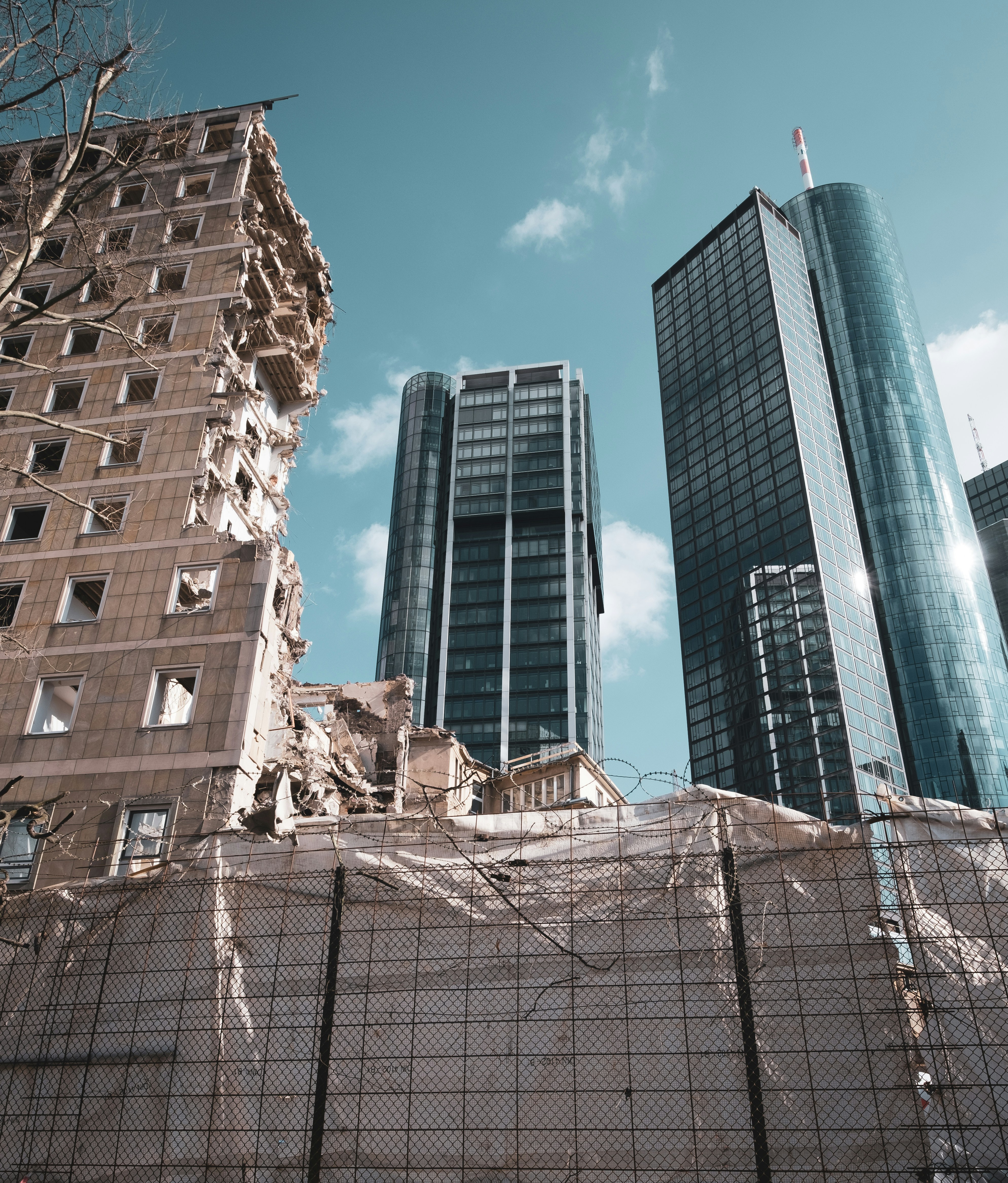 A partially demolished building stands in stark contrast to modern skyscrapers under a clear blue sky.