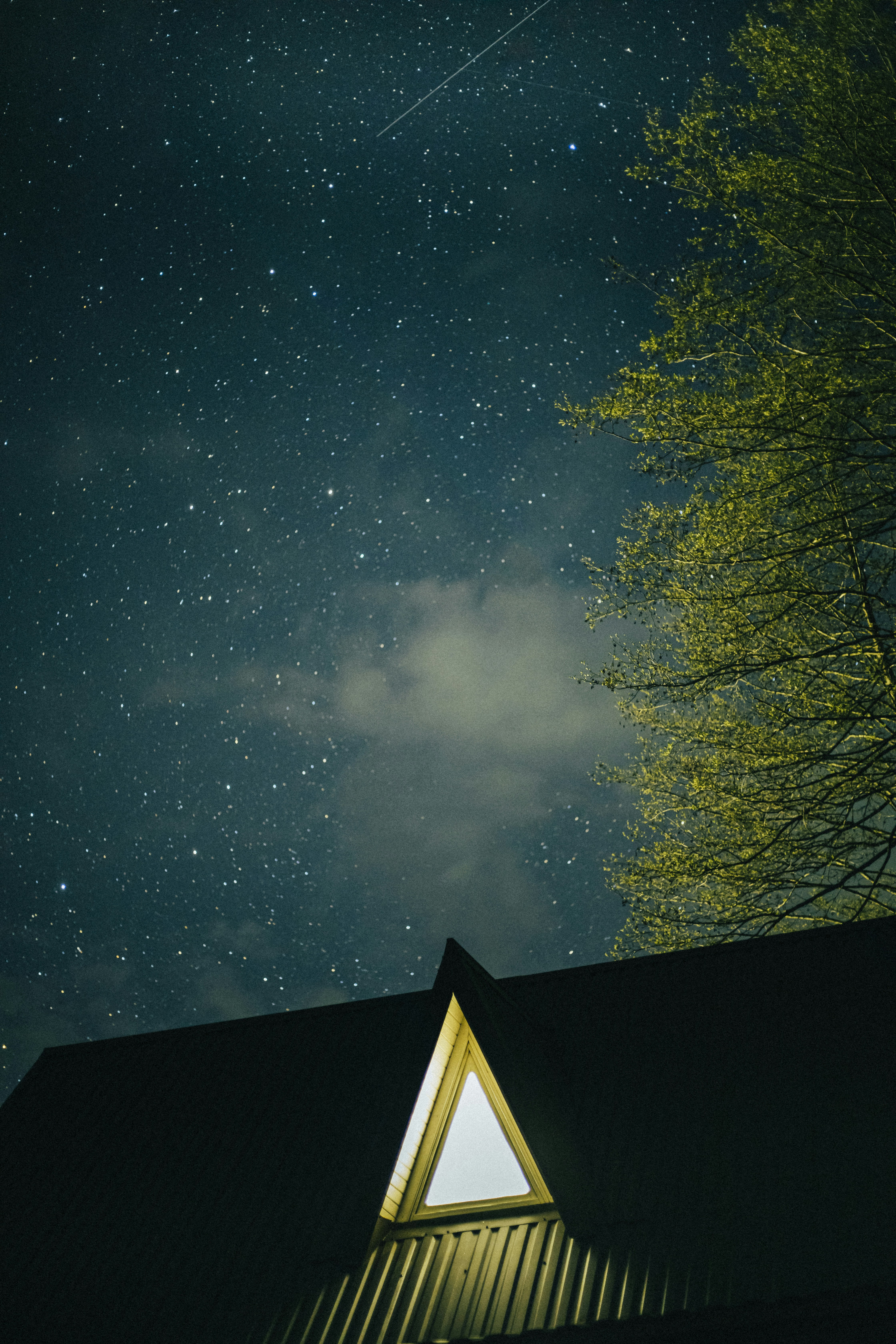 A cozy cabin under a starry sky, with a glowing window illuminating the dark surroundings. The serene atmosphere invites contemplation.