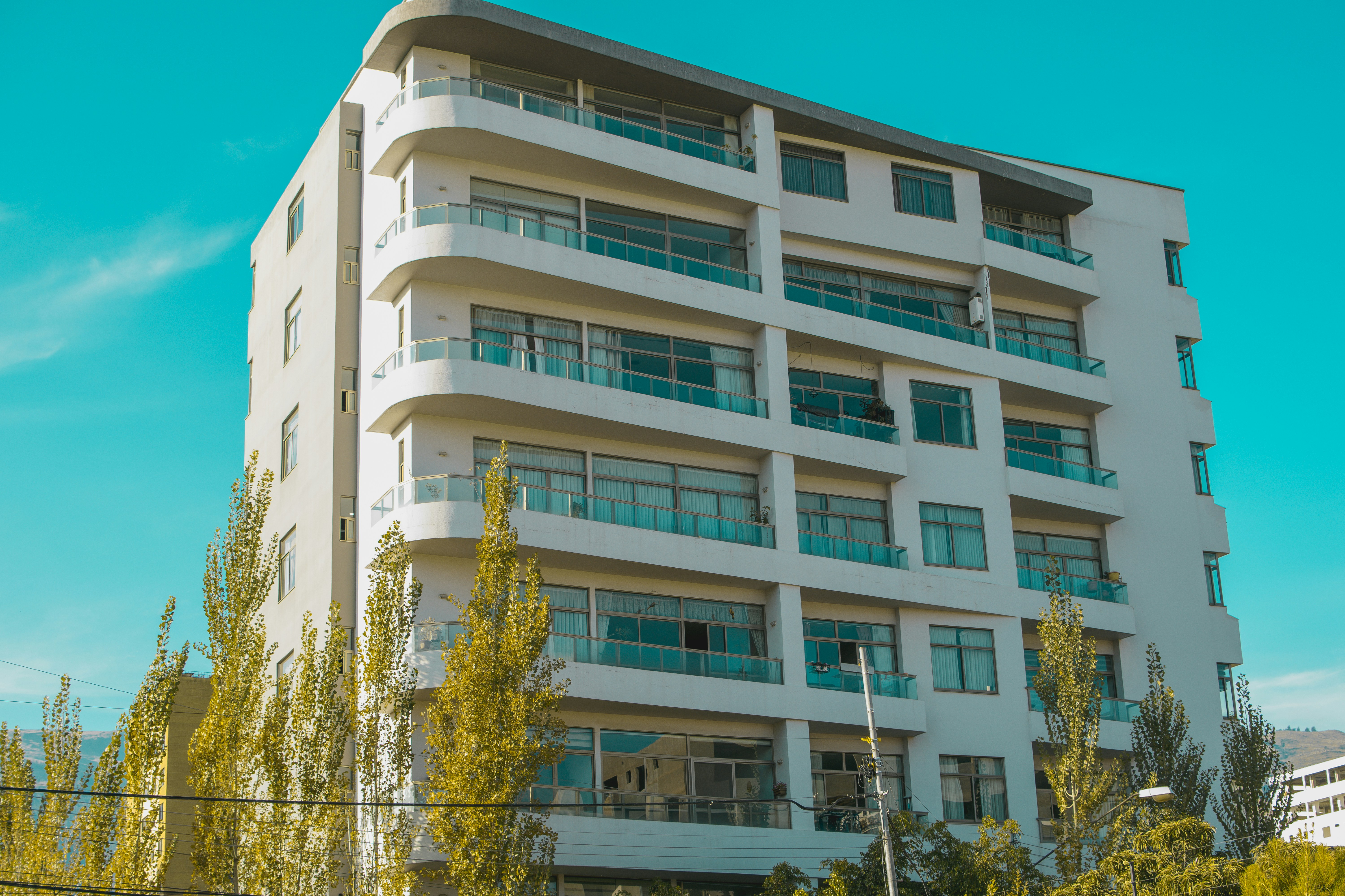 Mid-rise apartment building with a clean, modern design and large windows under a vibrant turquoise sky.