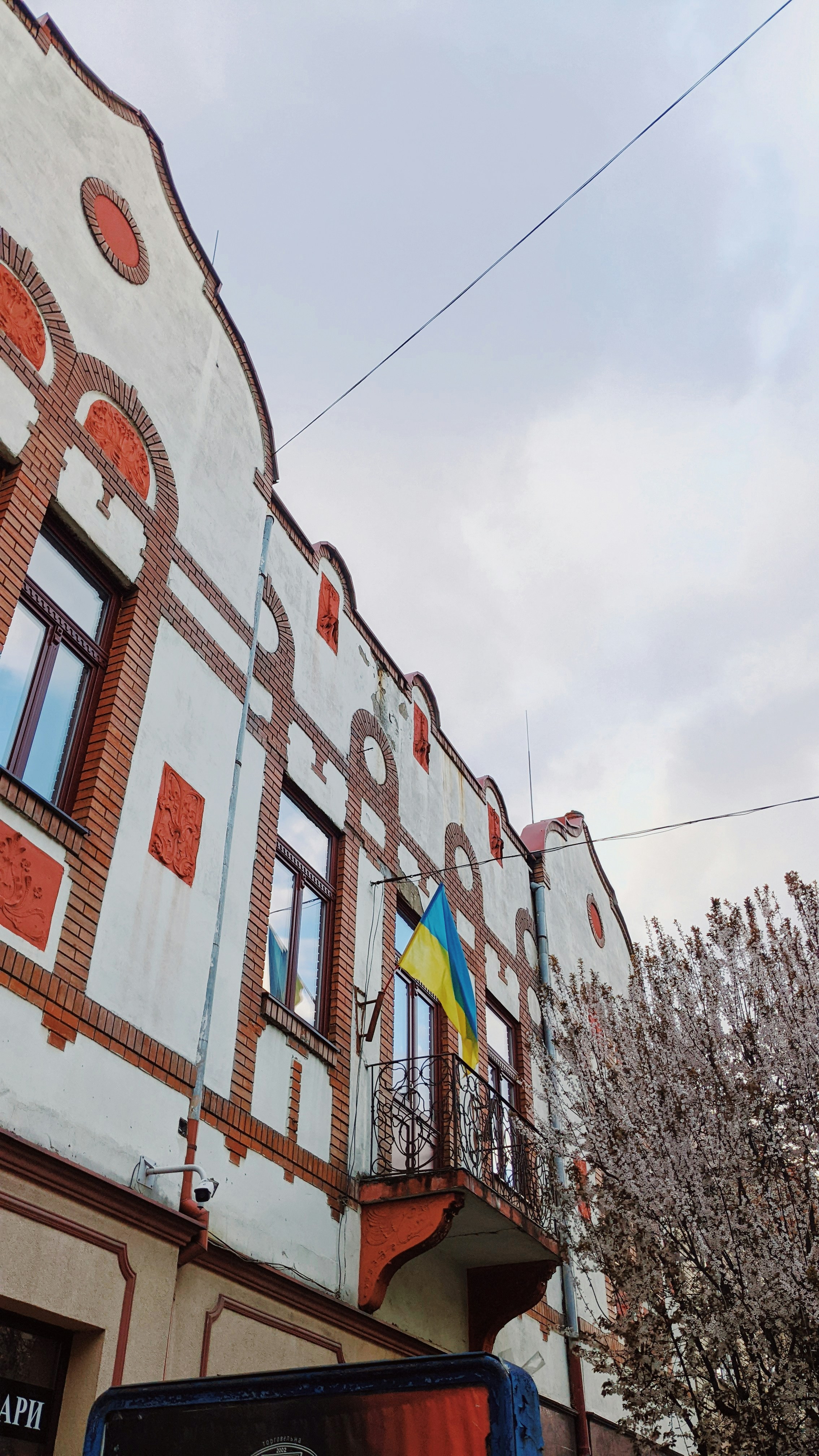 Ukrainian Flag Anchored on a Carved Balcony Amid Pastel Facade and Spring Blooms