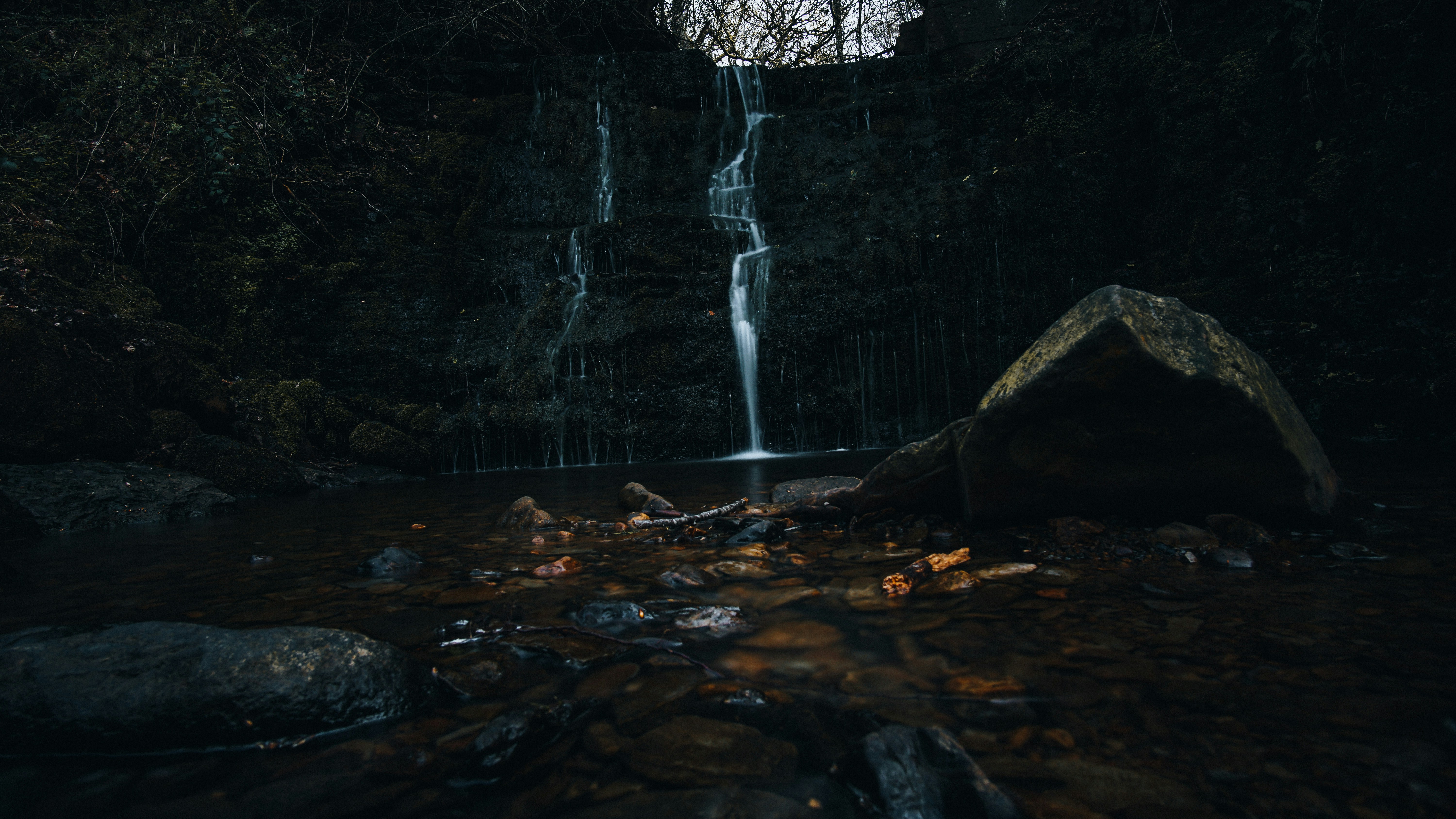 Waterfall cascading into a rocky pool surrounded by dense forest.