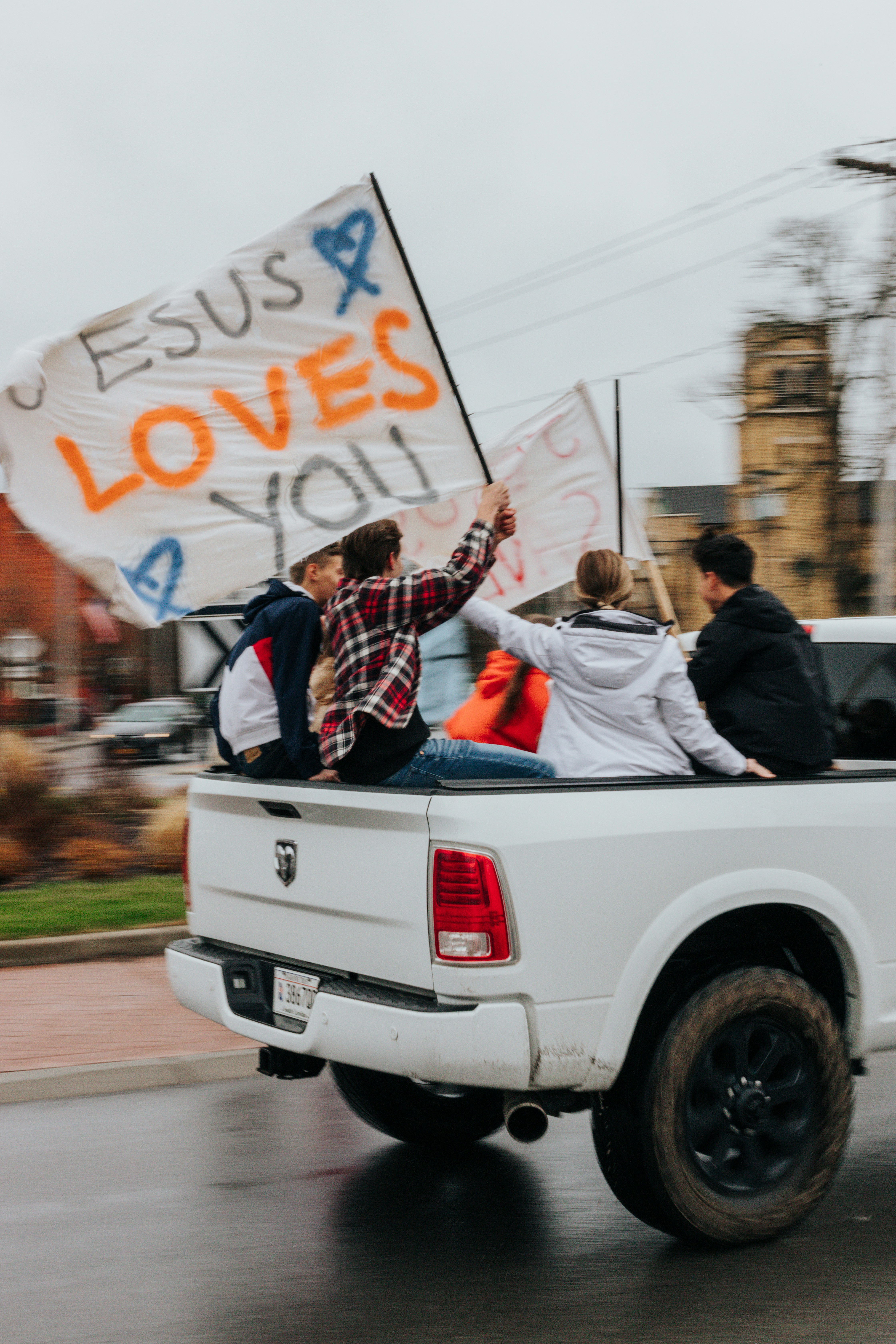 Rally in Blur: Youth in a White Pickup Carry a Sign Through a Moving Street